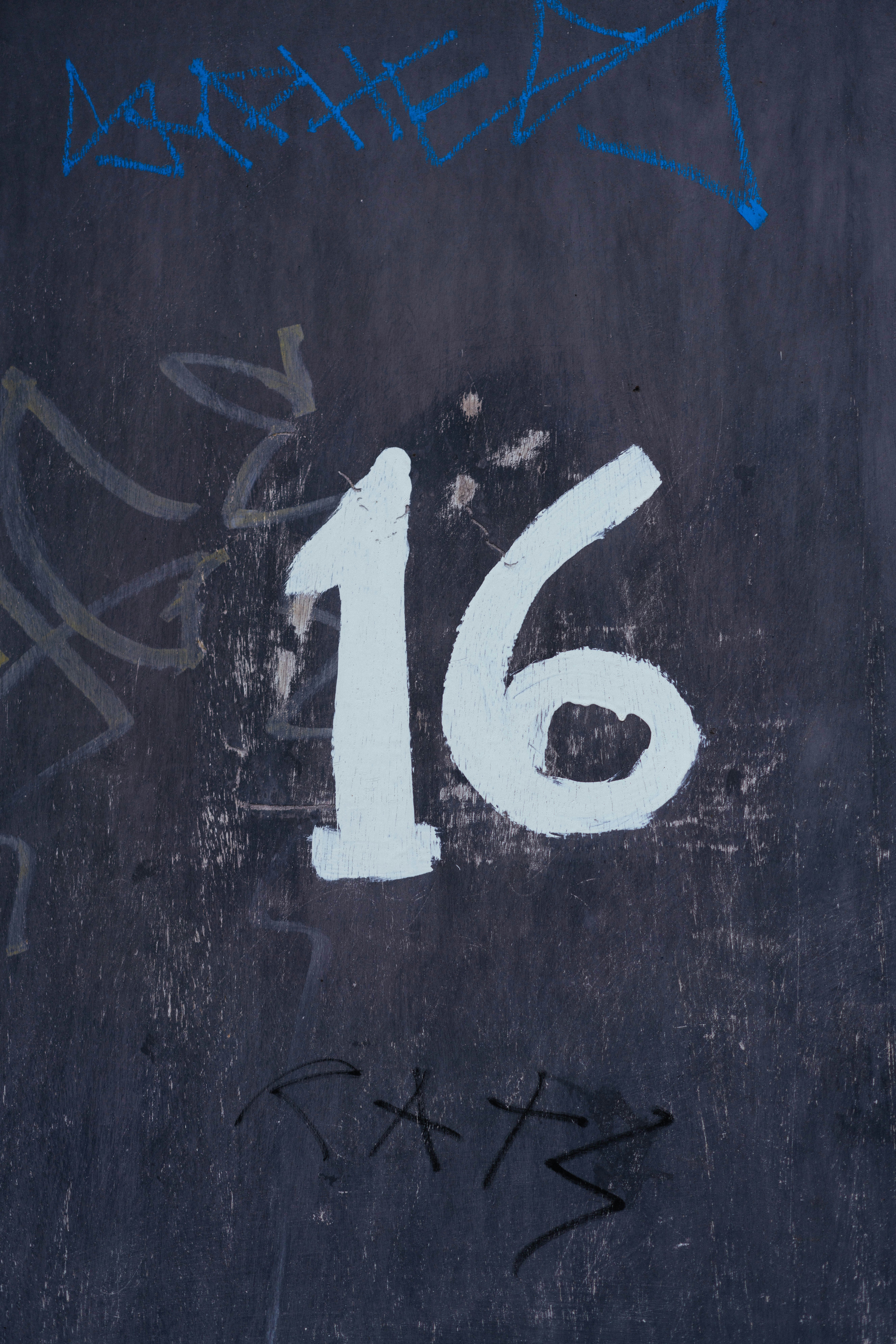 Number 16 on a weathered surface: graffiti layers and chipped plaster