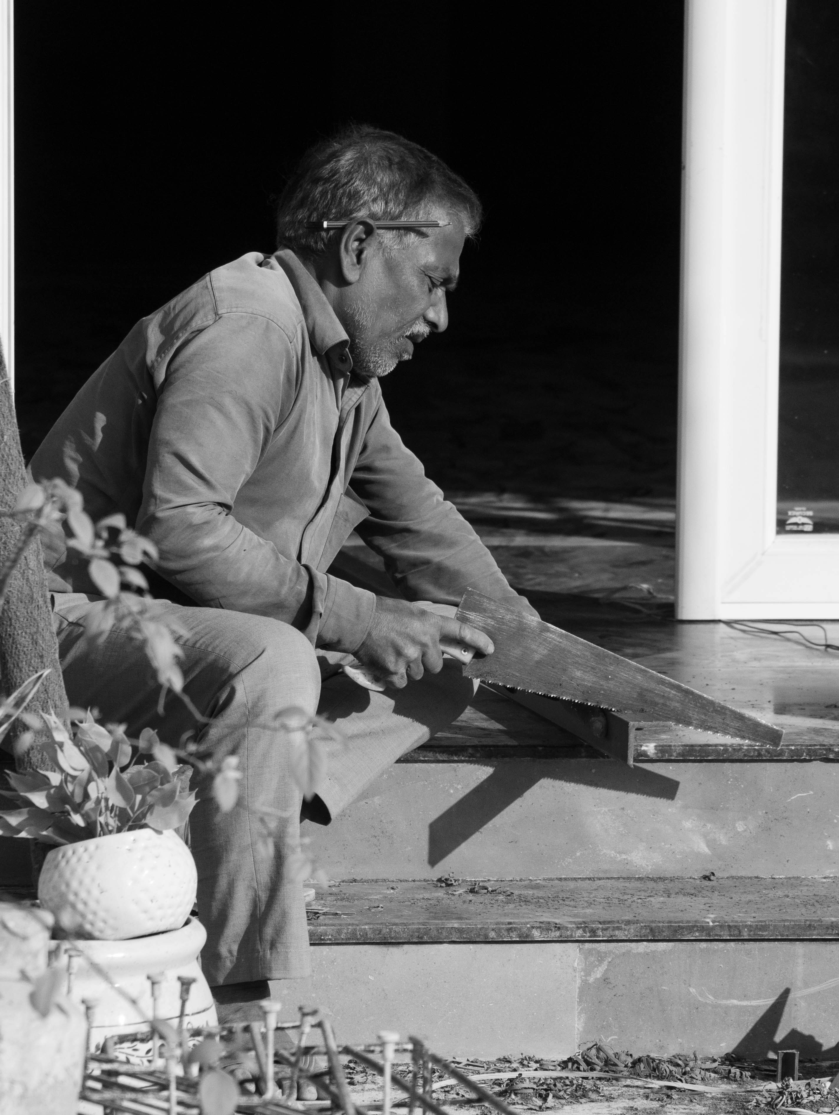 Portrait of a craftsman at work: slicing wood by dim doorway light