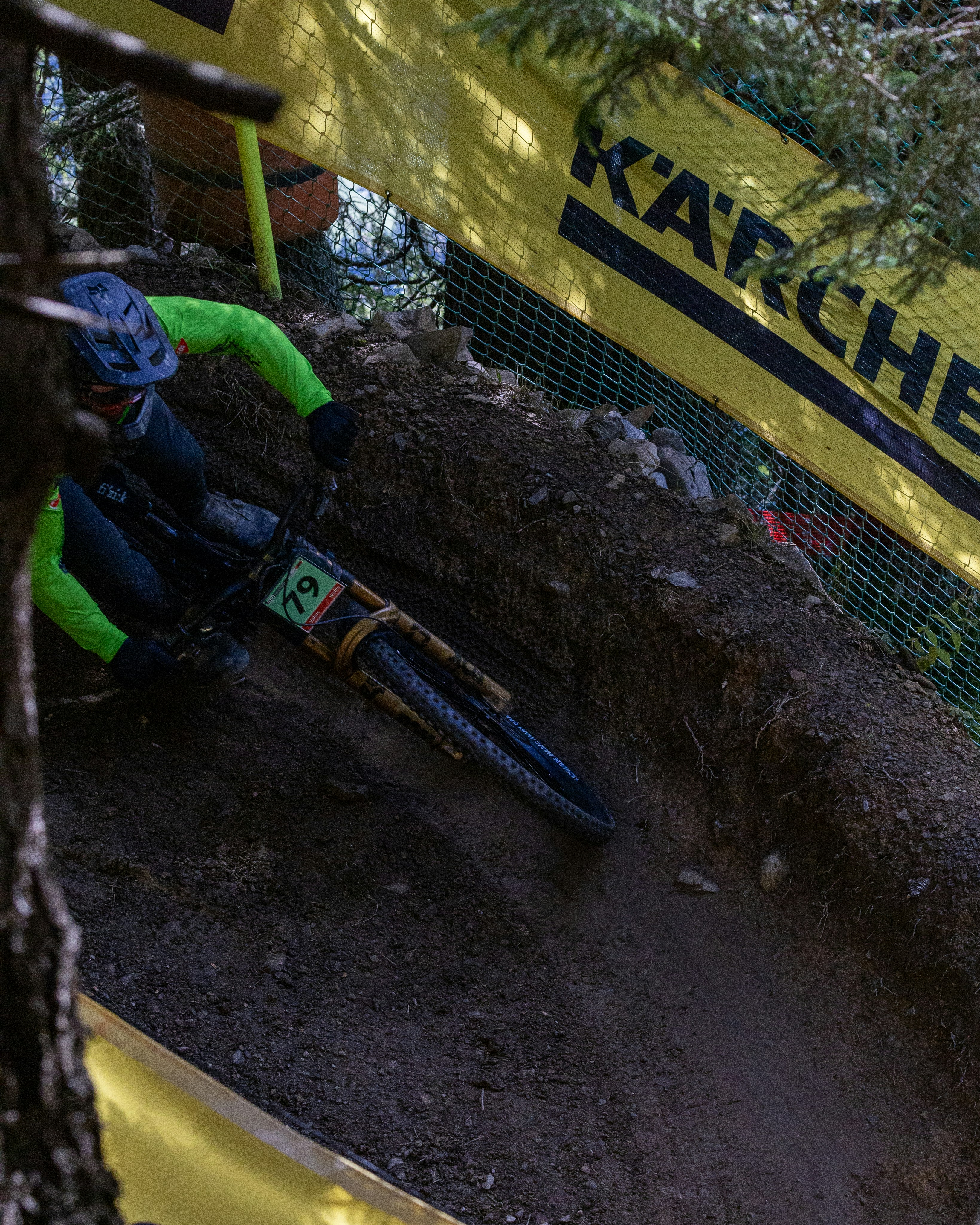 Low-angled descent: rider carving a muddy curve under yellow safety banner