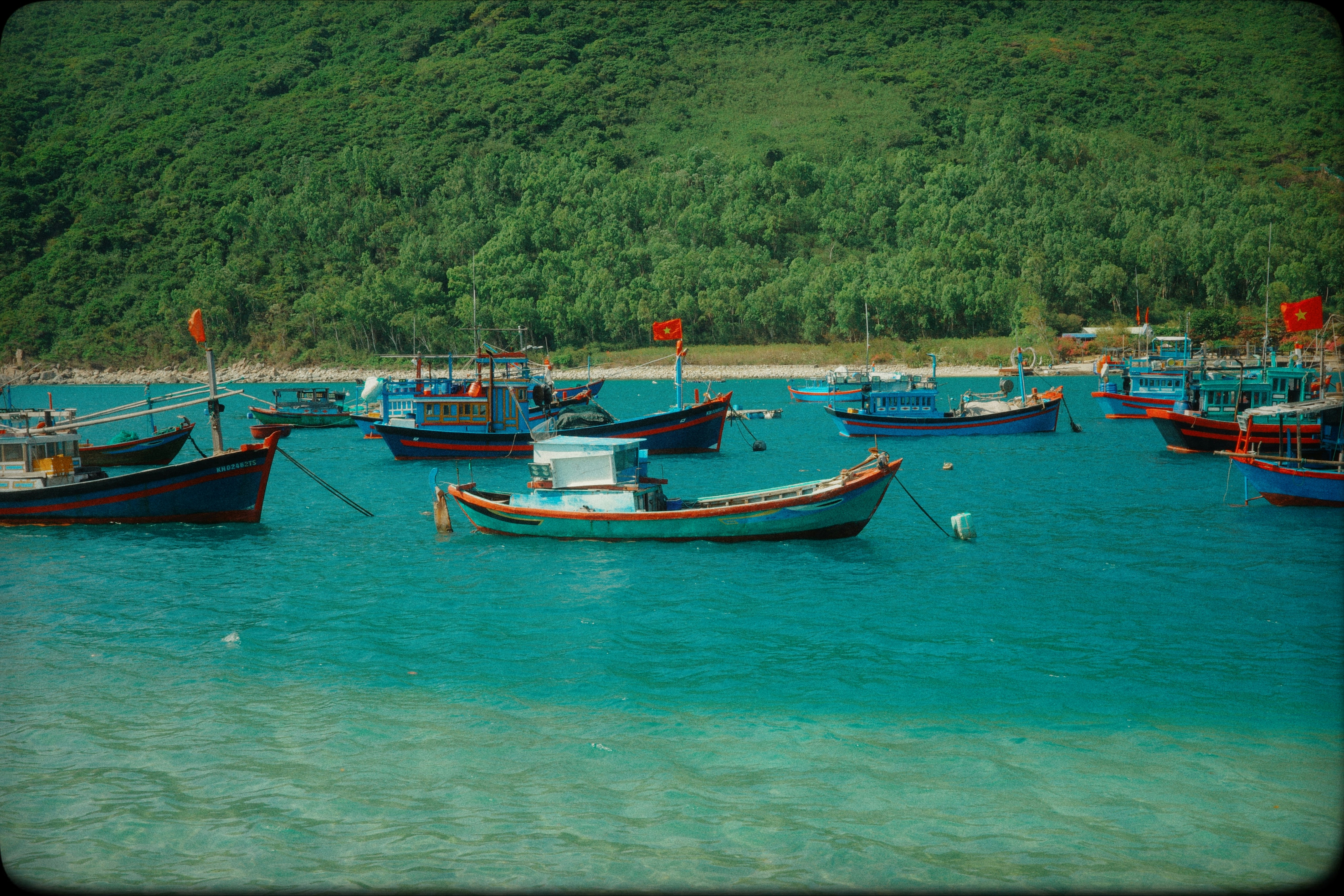 Boats at turquoise bay under emerald hillside