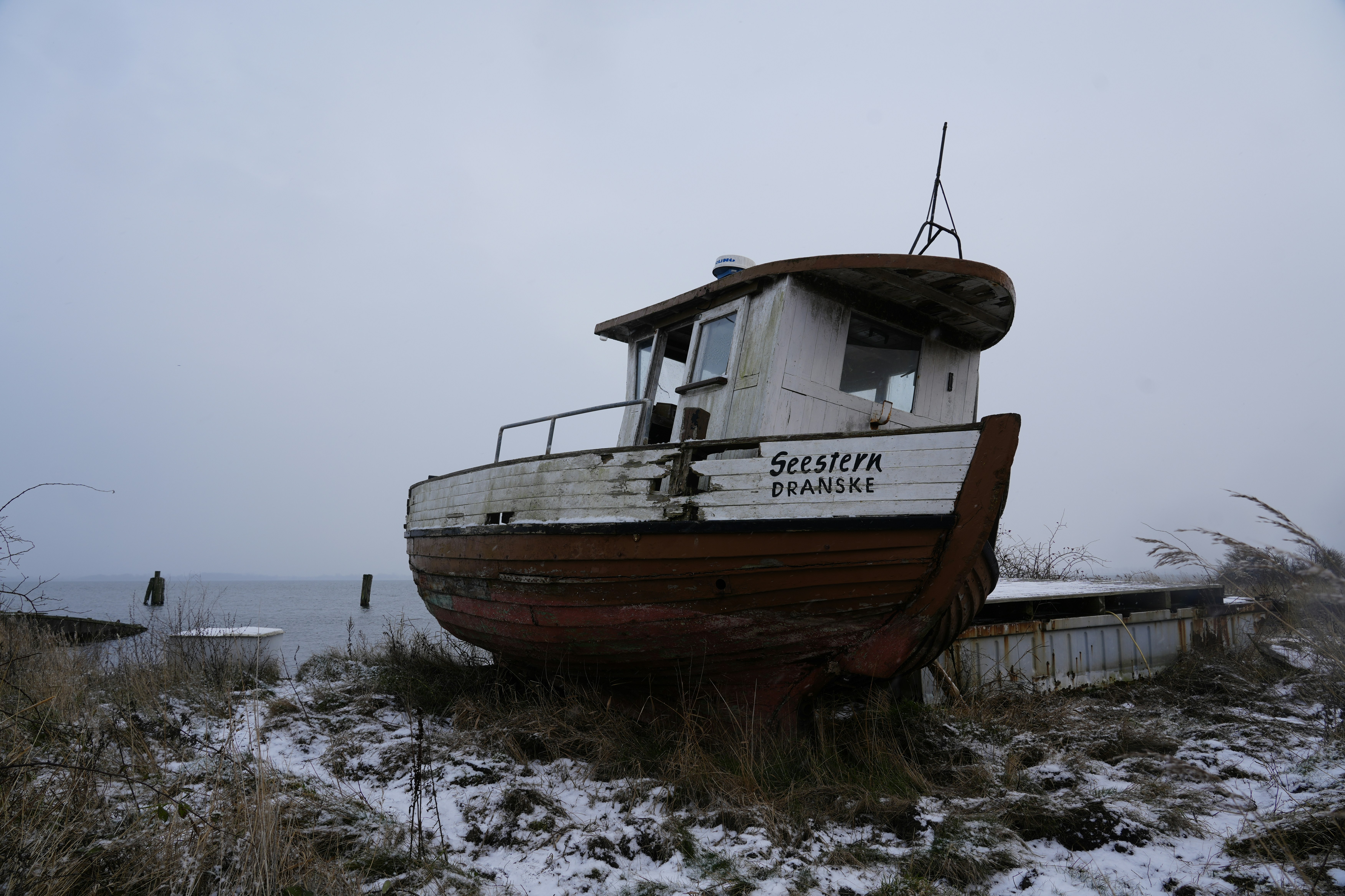 Beached Boat on a Snow-Dusted Shore: Weathered Hull and Quiet Dusk