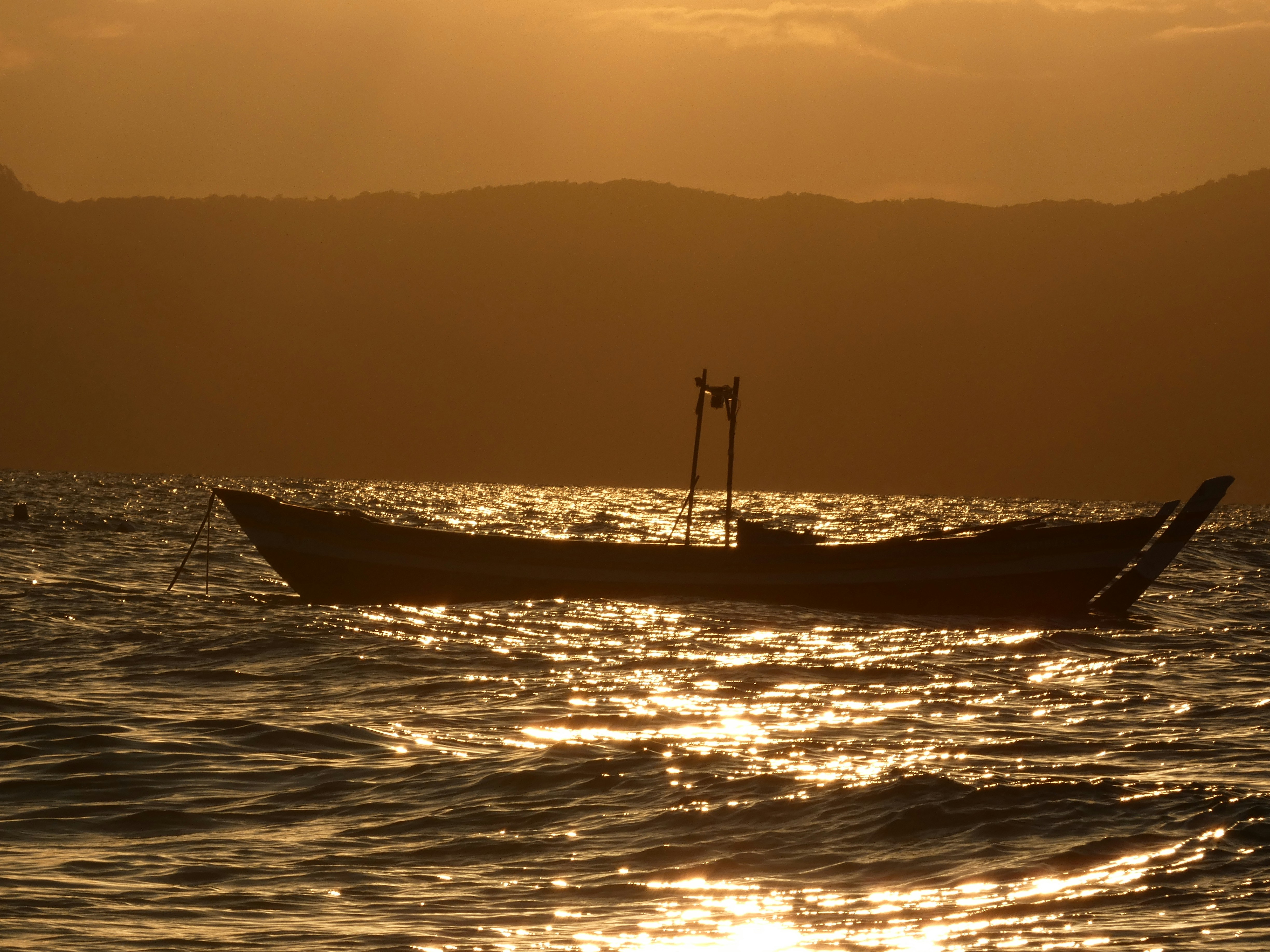 Silhouette at Golden Hour: A Lone Boat Gliding Across Shimmering Seas