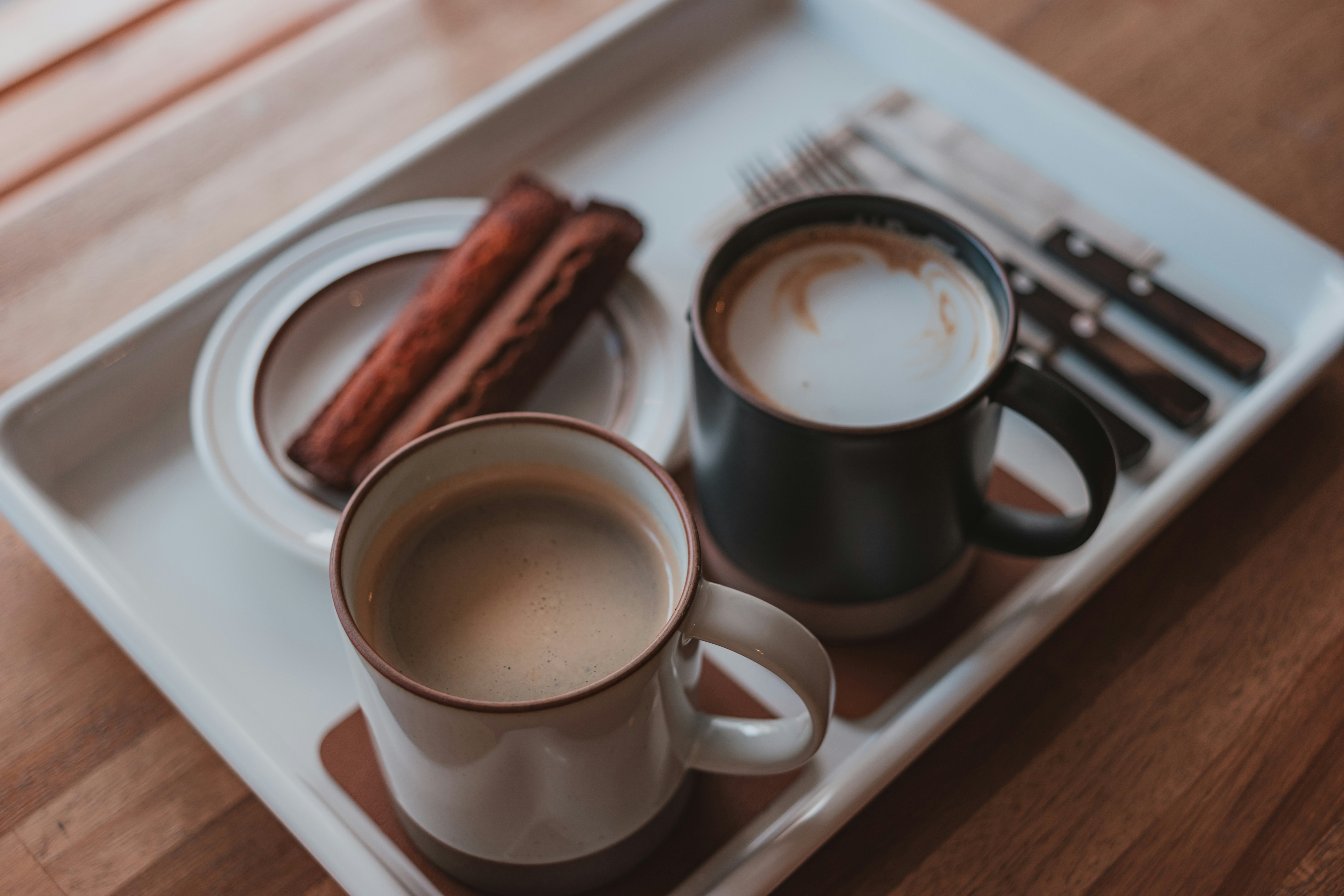 Two cups of coffee and pastries on a tray.