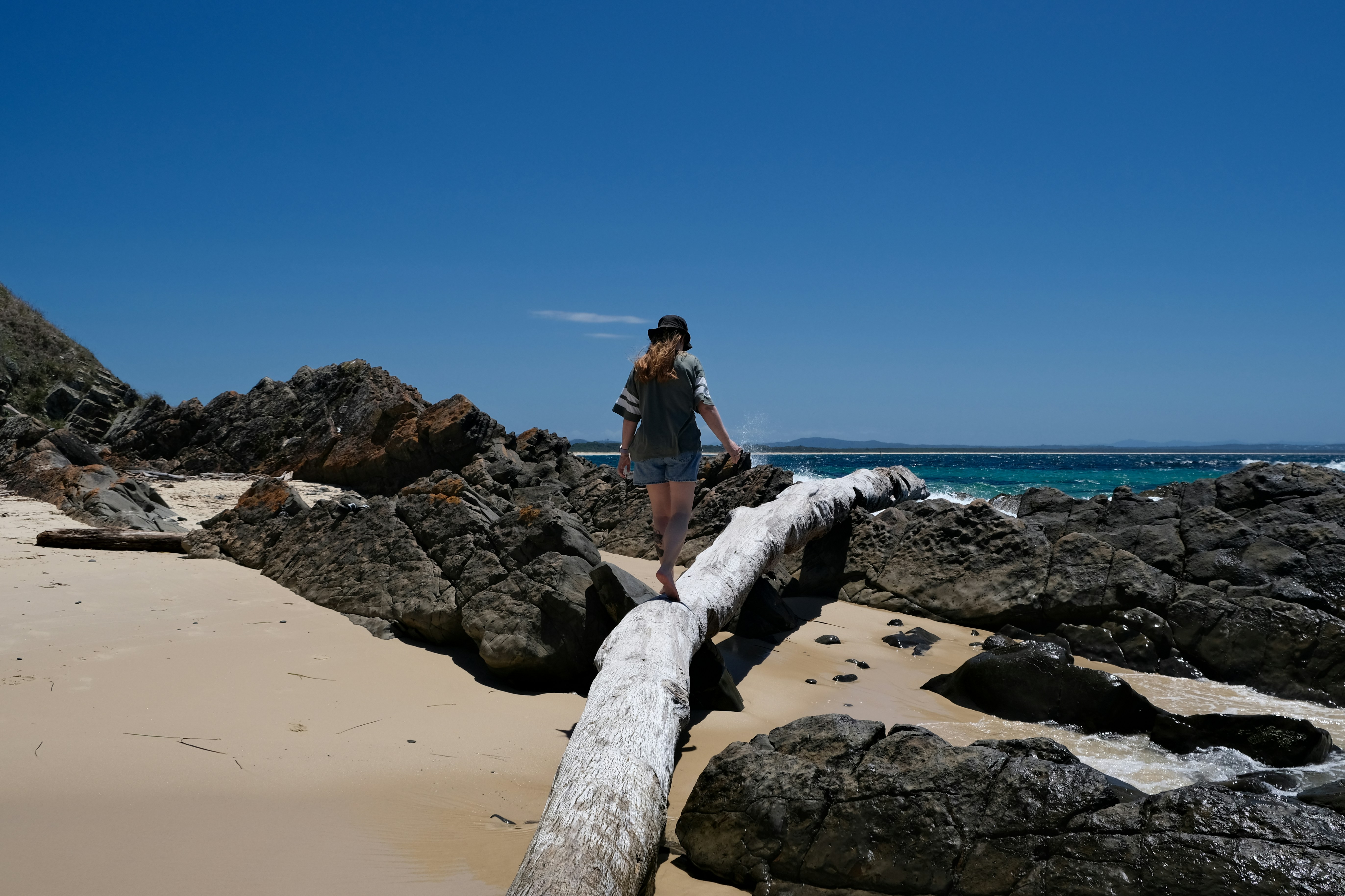 Traveler on a sunlit driftwood bridge over rugged beach rocks