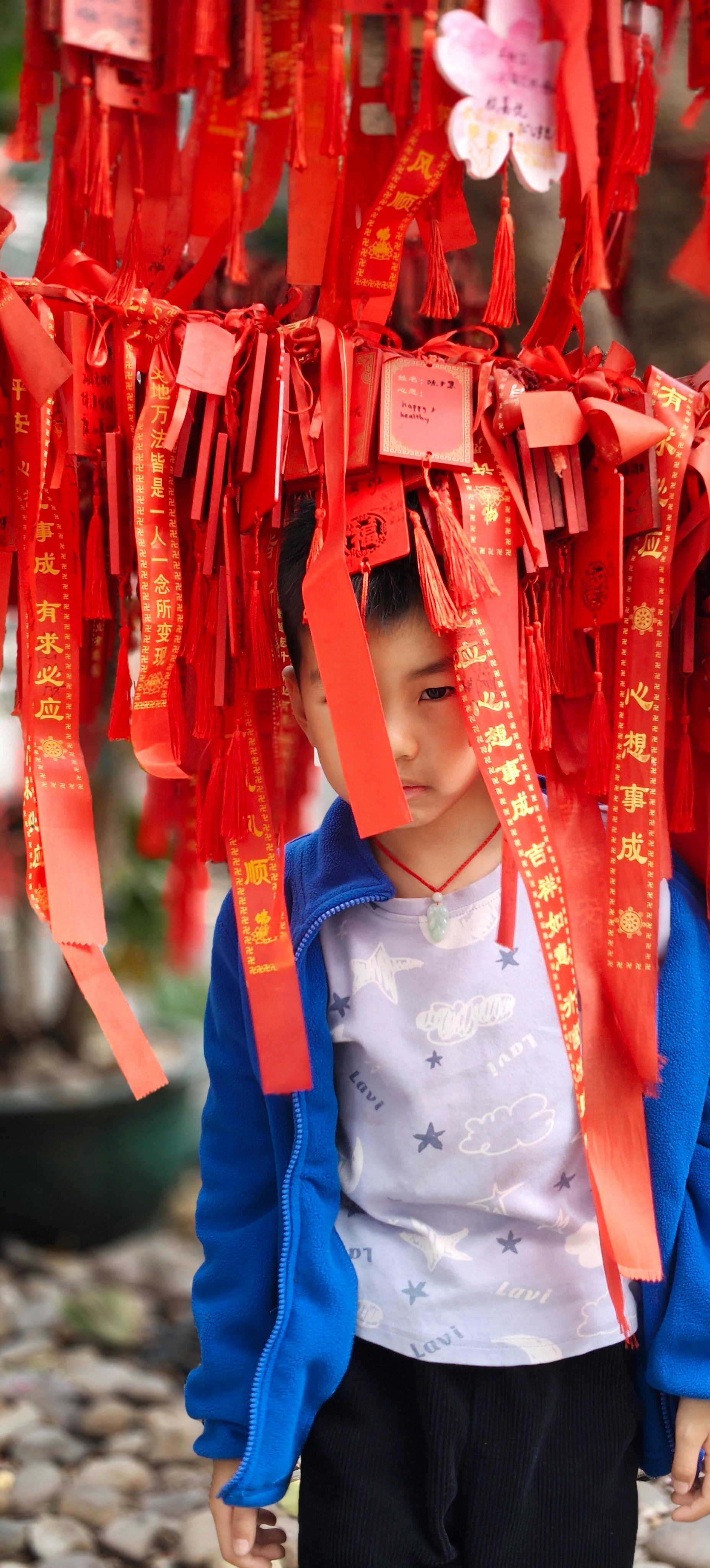 Young child stands amidst red prayer ribbons