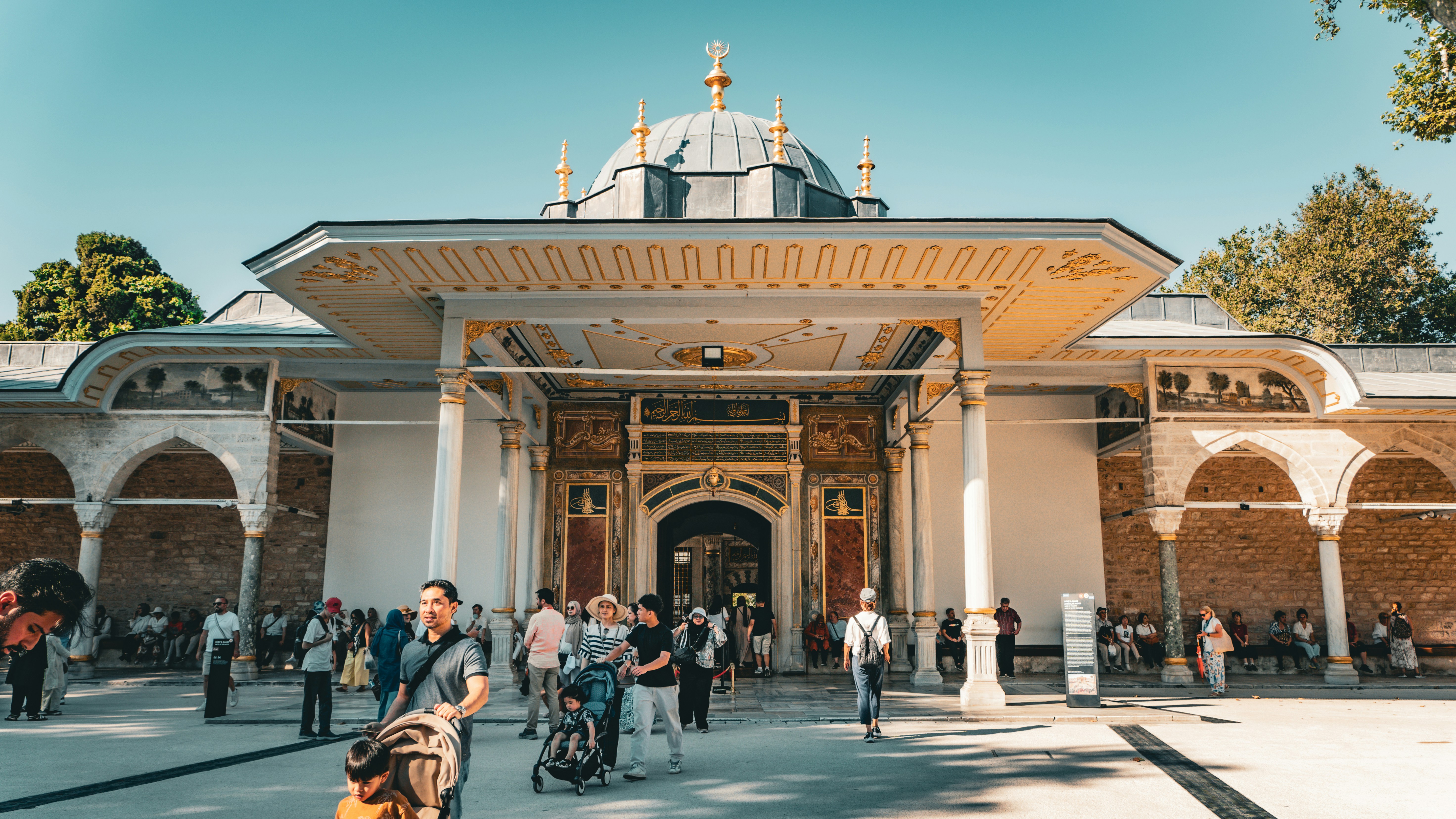 Sunlit Gatehouse: Visitors Converge at a Historic Courtyard Portal