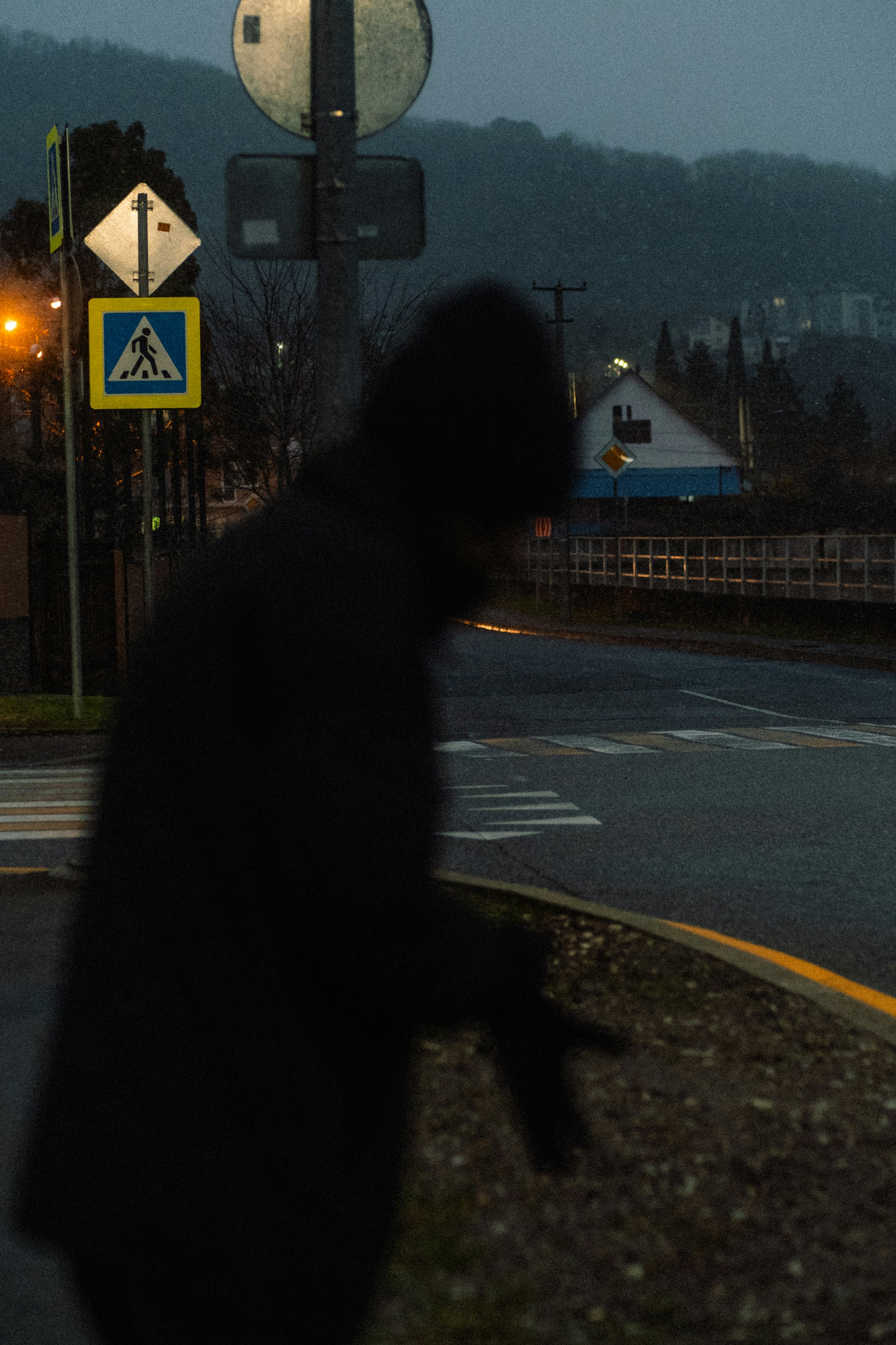  silhouetted figure crossing at dusk by a quiet road