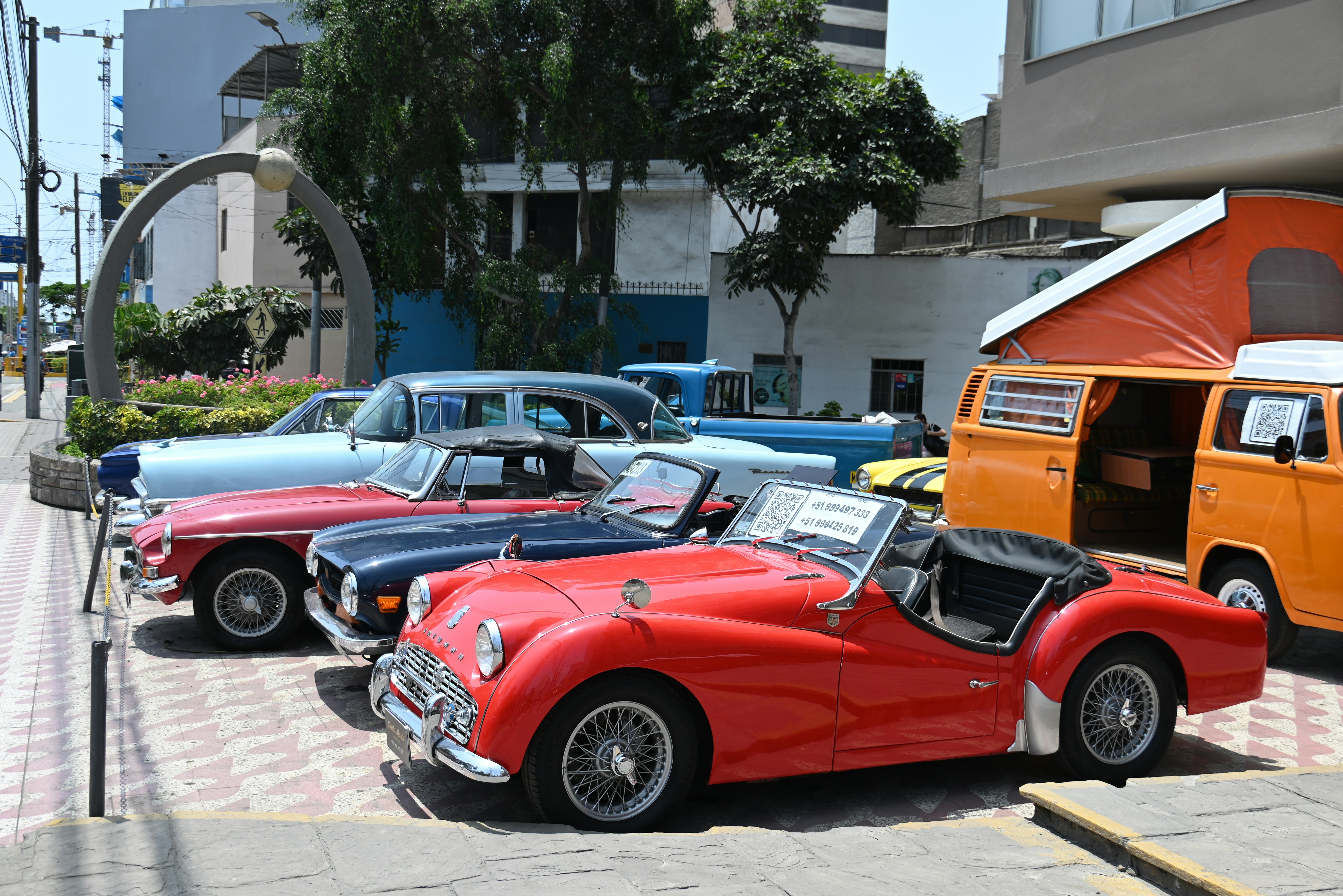 Red Convertible Parade: Classic Cars Parked by a City Plaza