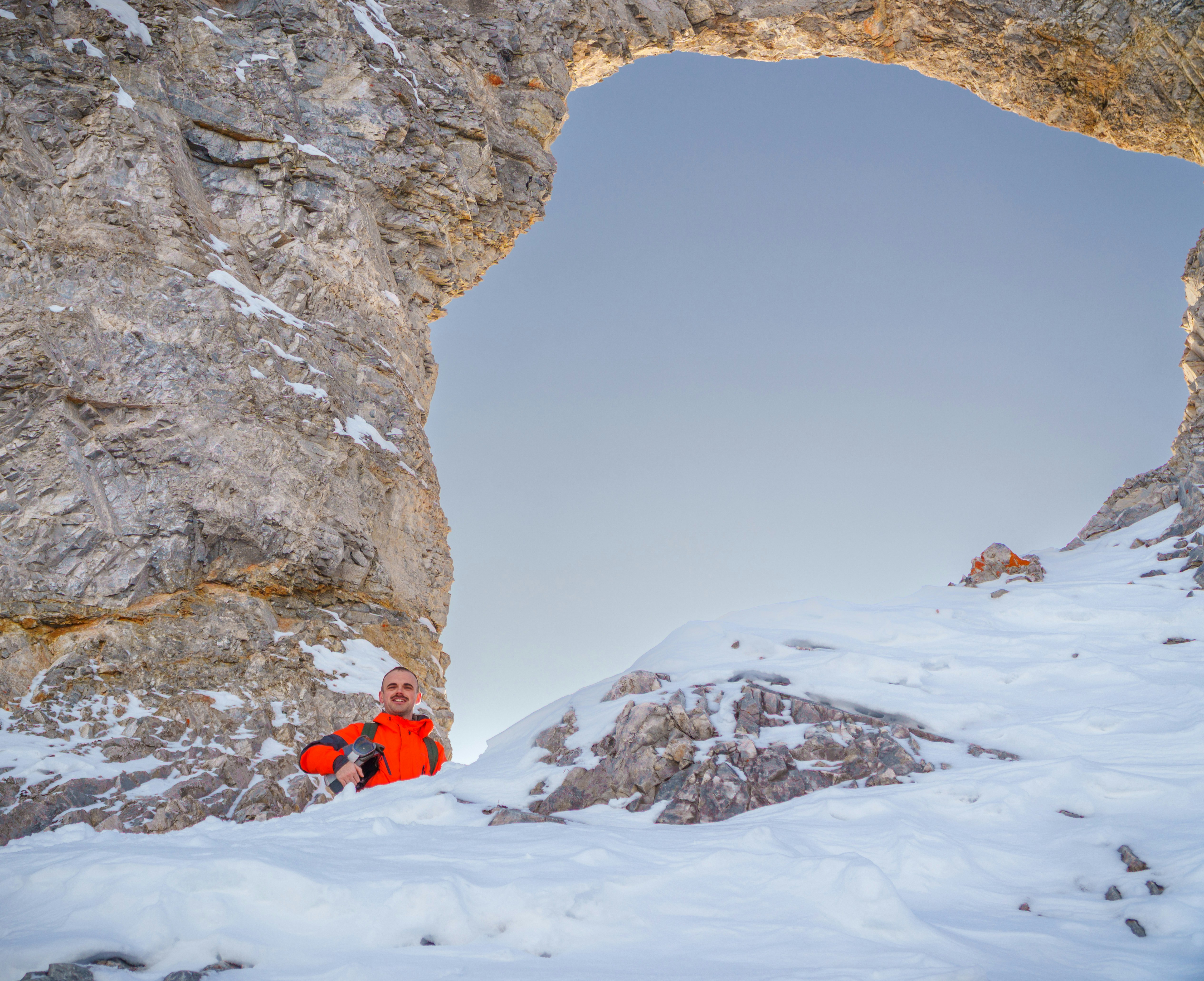 Red-clad climber in a snow canyon under a rock arch