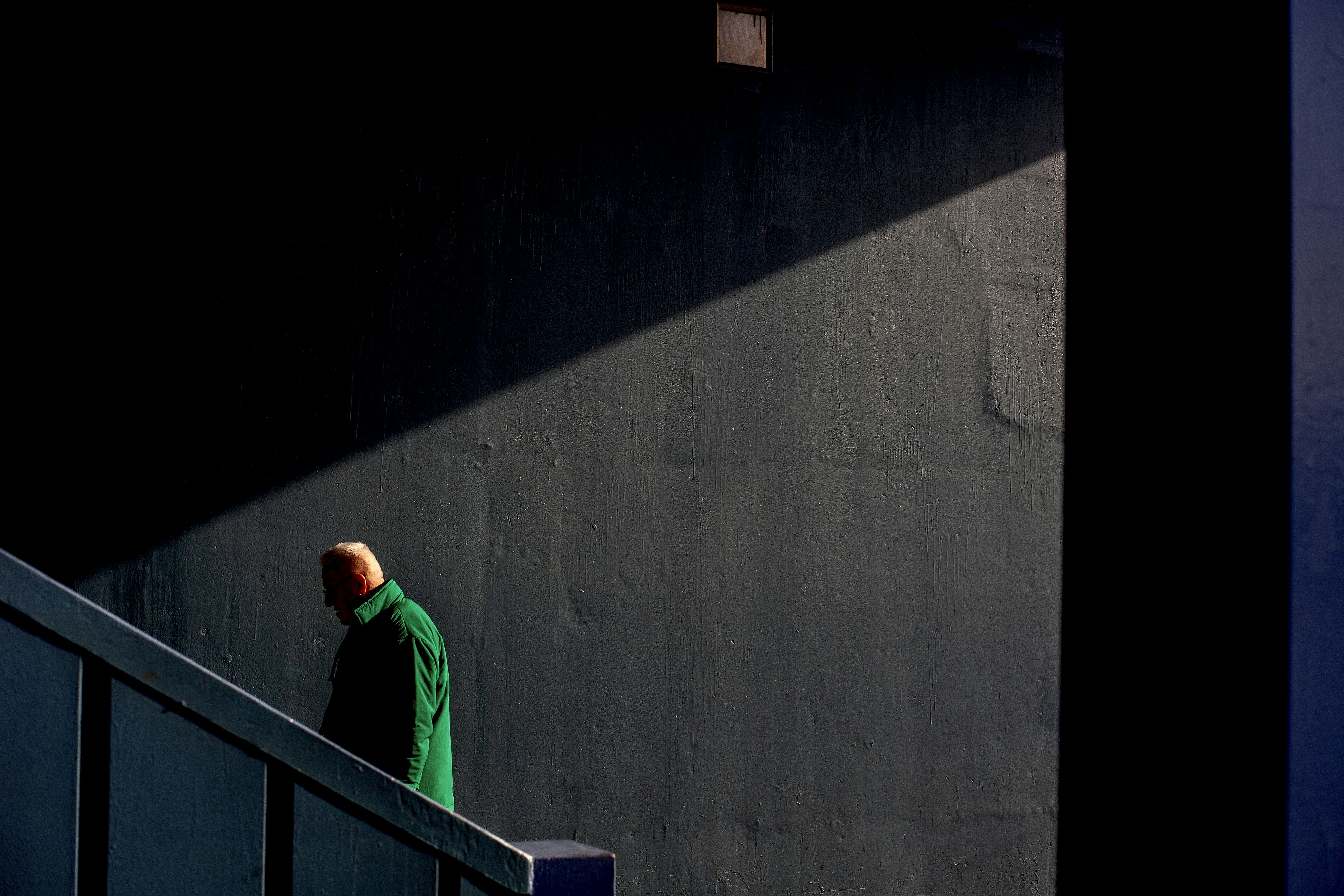 Shadowed Walkway: A Lone Figure in Green Descent