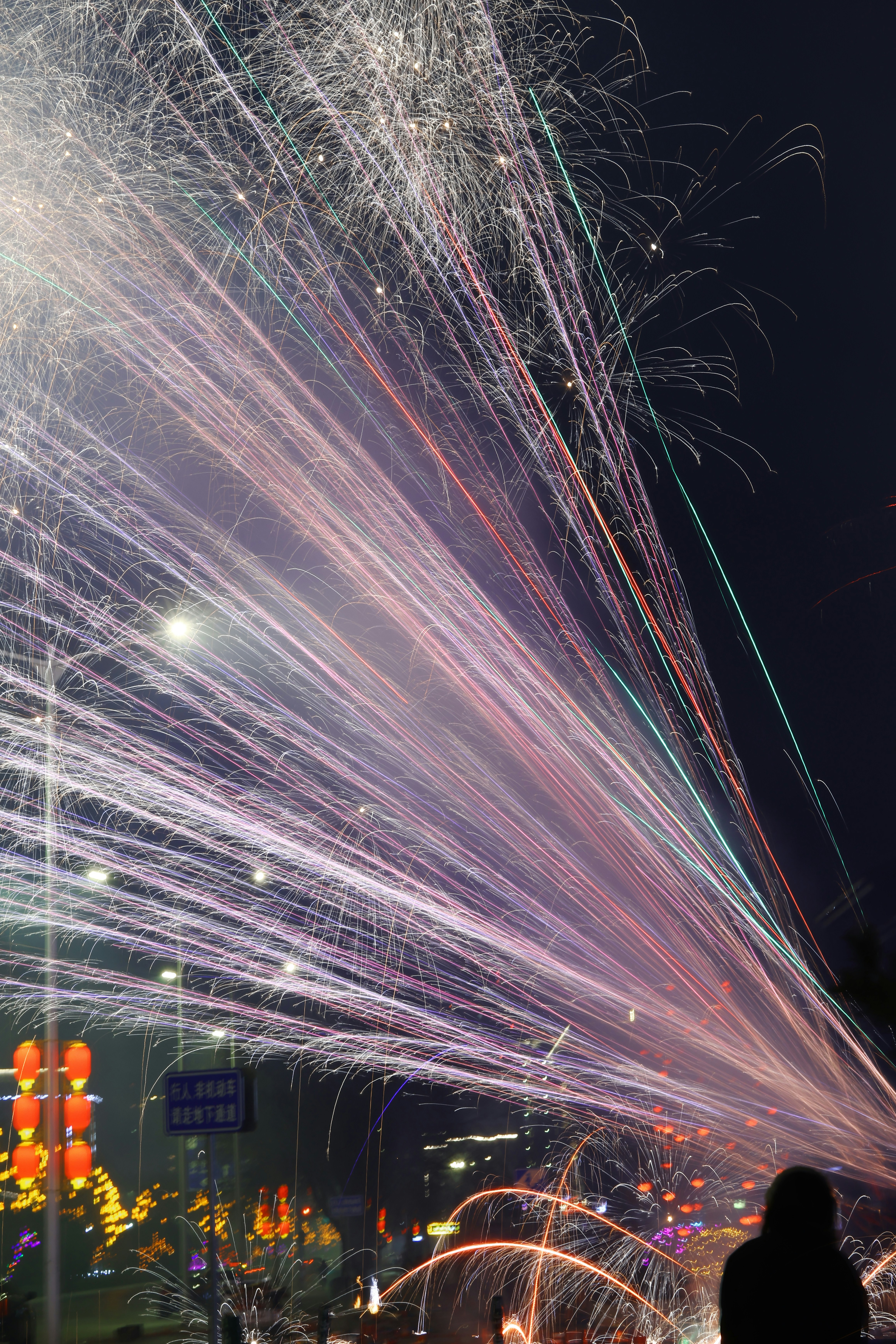 Night Sky Mosaic: Fireworks Arcing Over a Busier Street