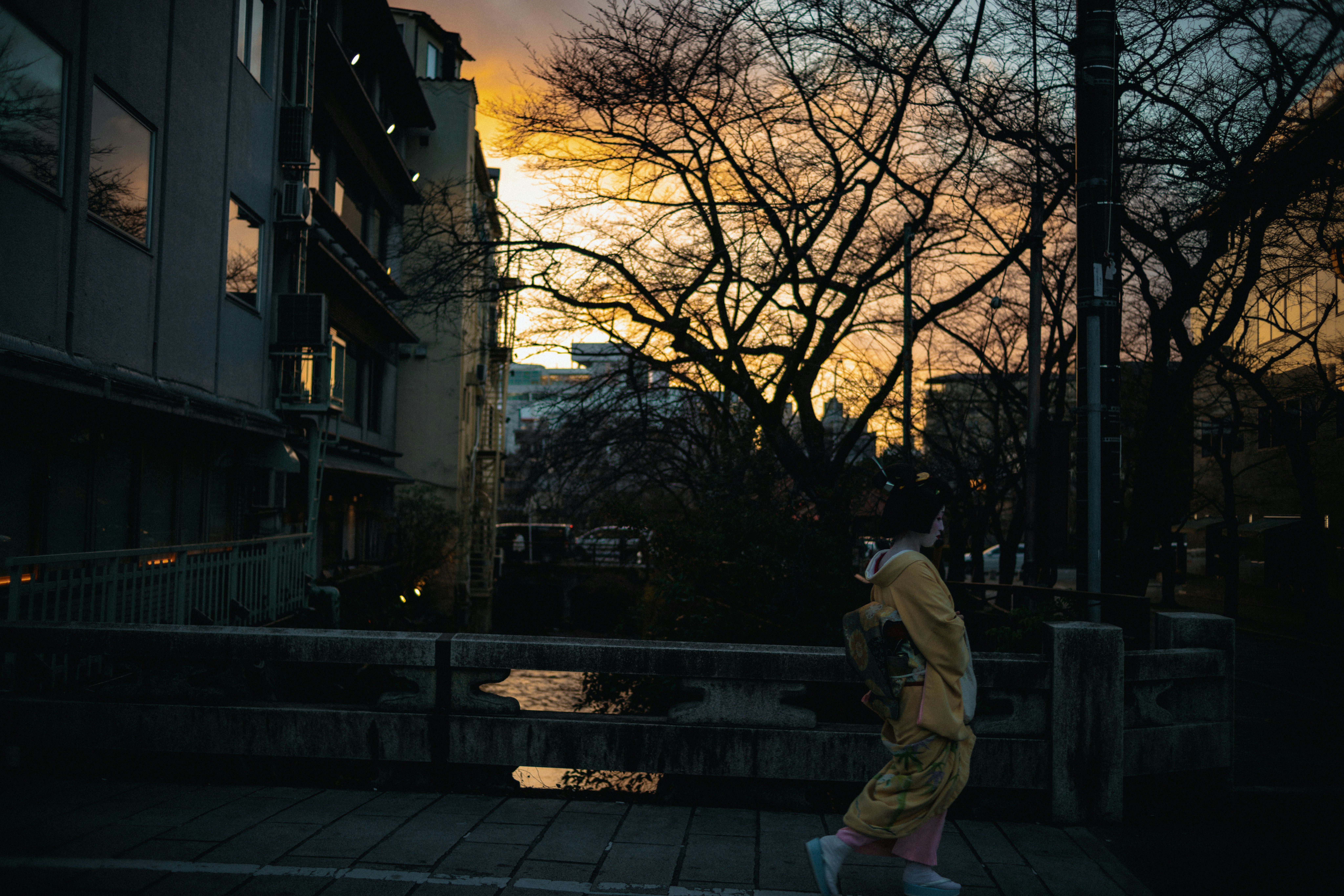 Amber Dusk Run: A figure in a yellow coat glides along a shadowed riverside path