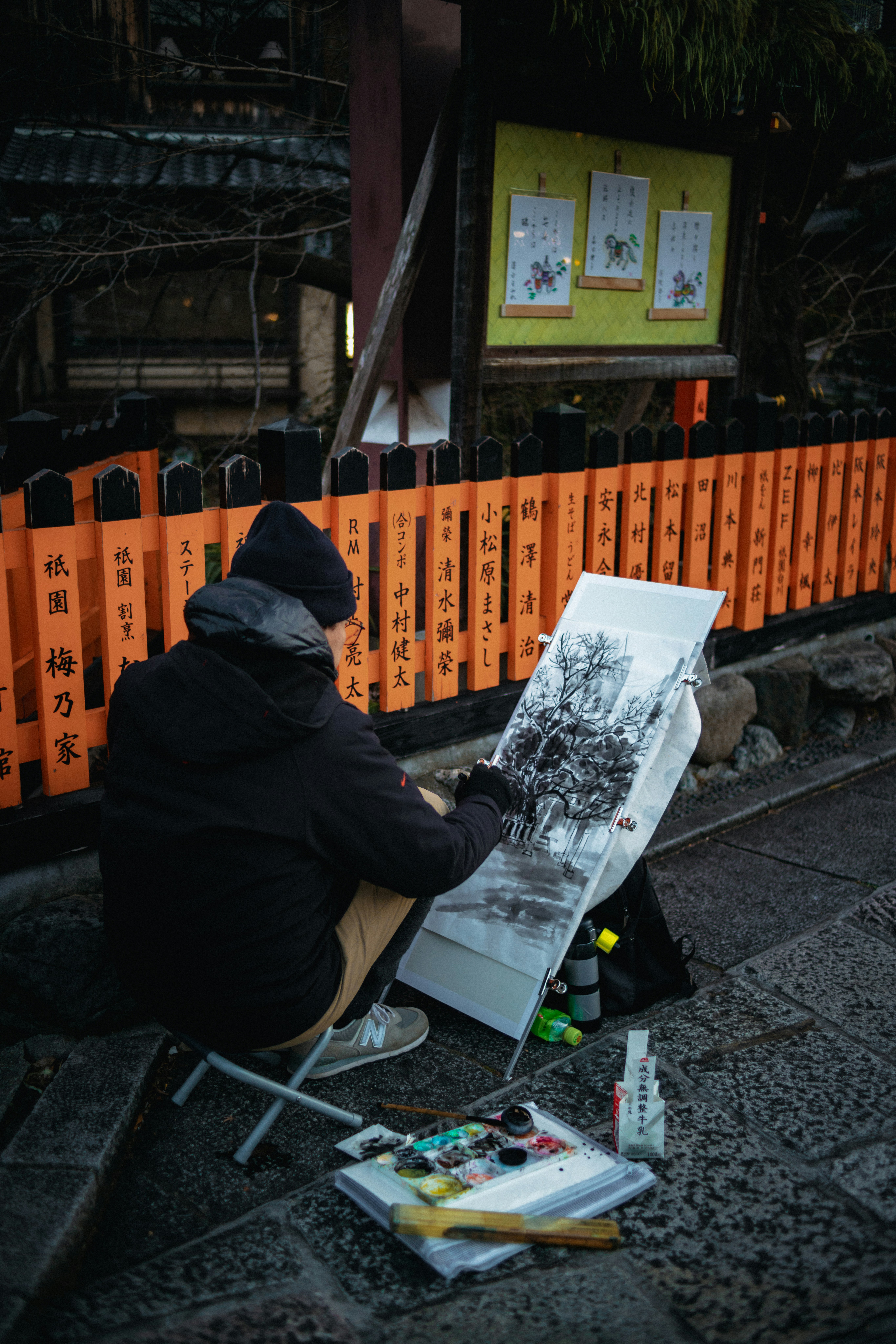 Sketching in the Lantern Alley: An Artist at Work by the Orange Slats