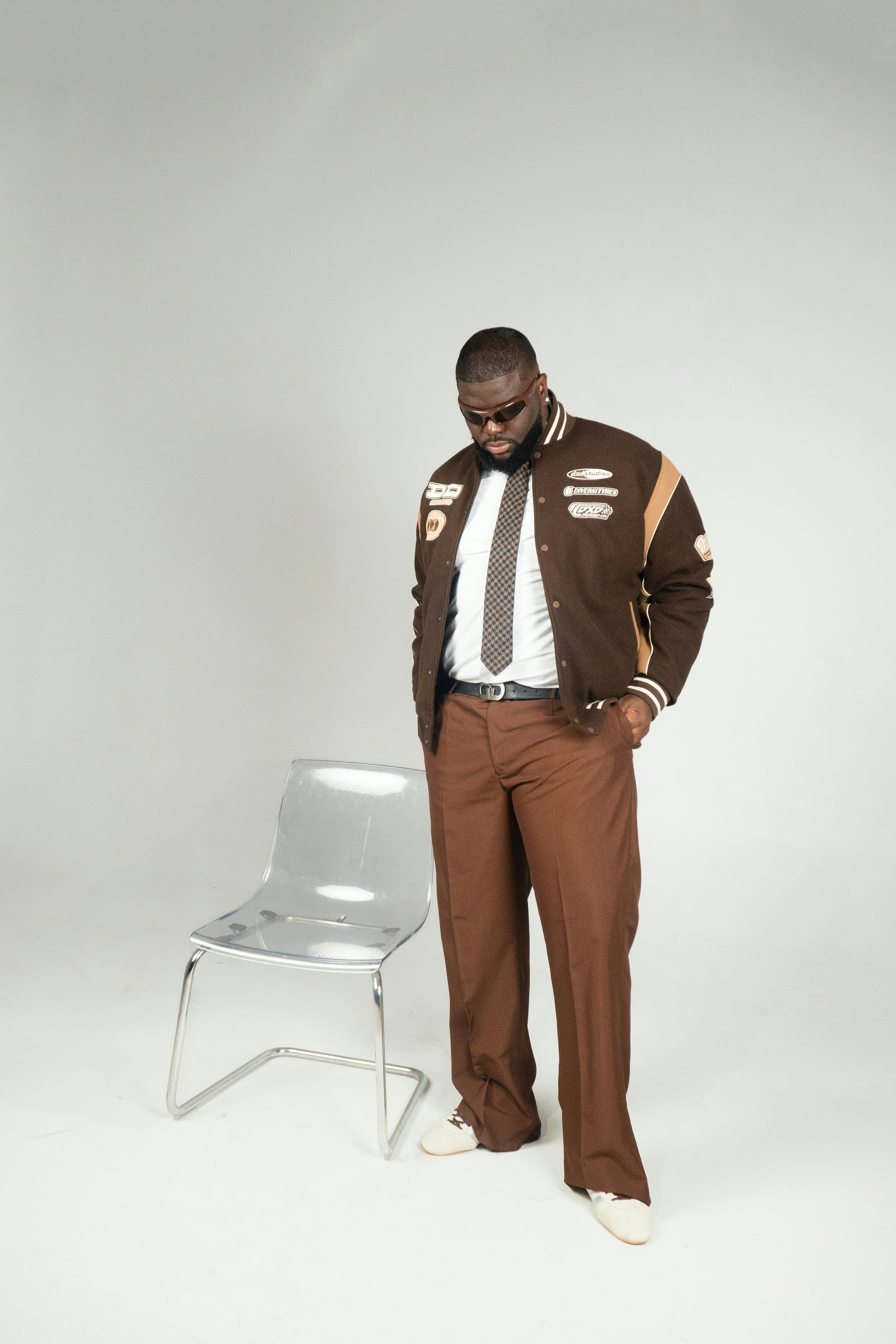 Stylish silhouette: a man in retro brown varsity jacket posing beside a transparent chair