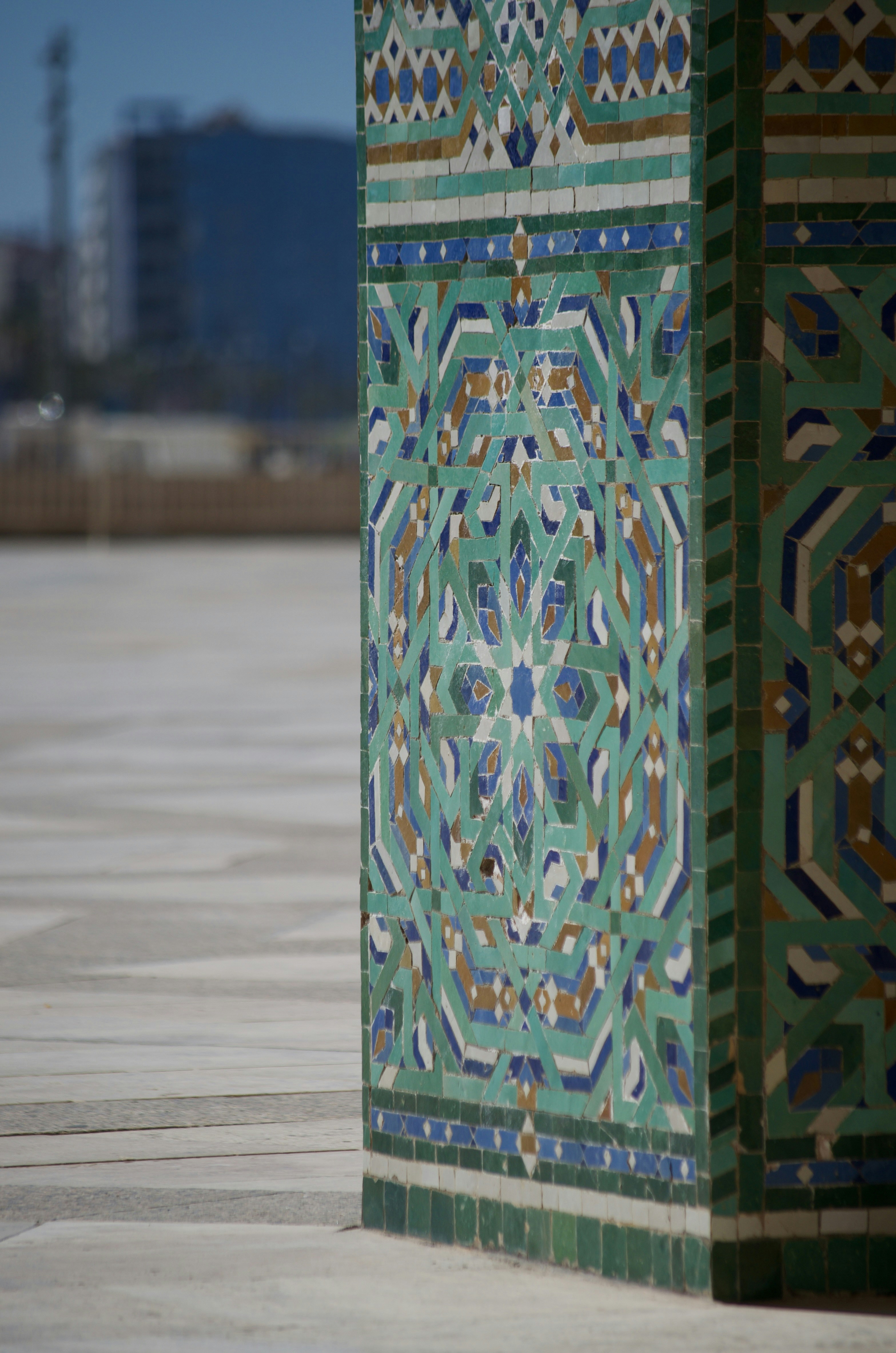 Geometric Mosaic Pillar: Green, Blue, and Gold Patterns in Sunlit Tilework