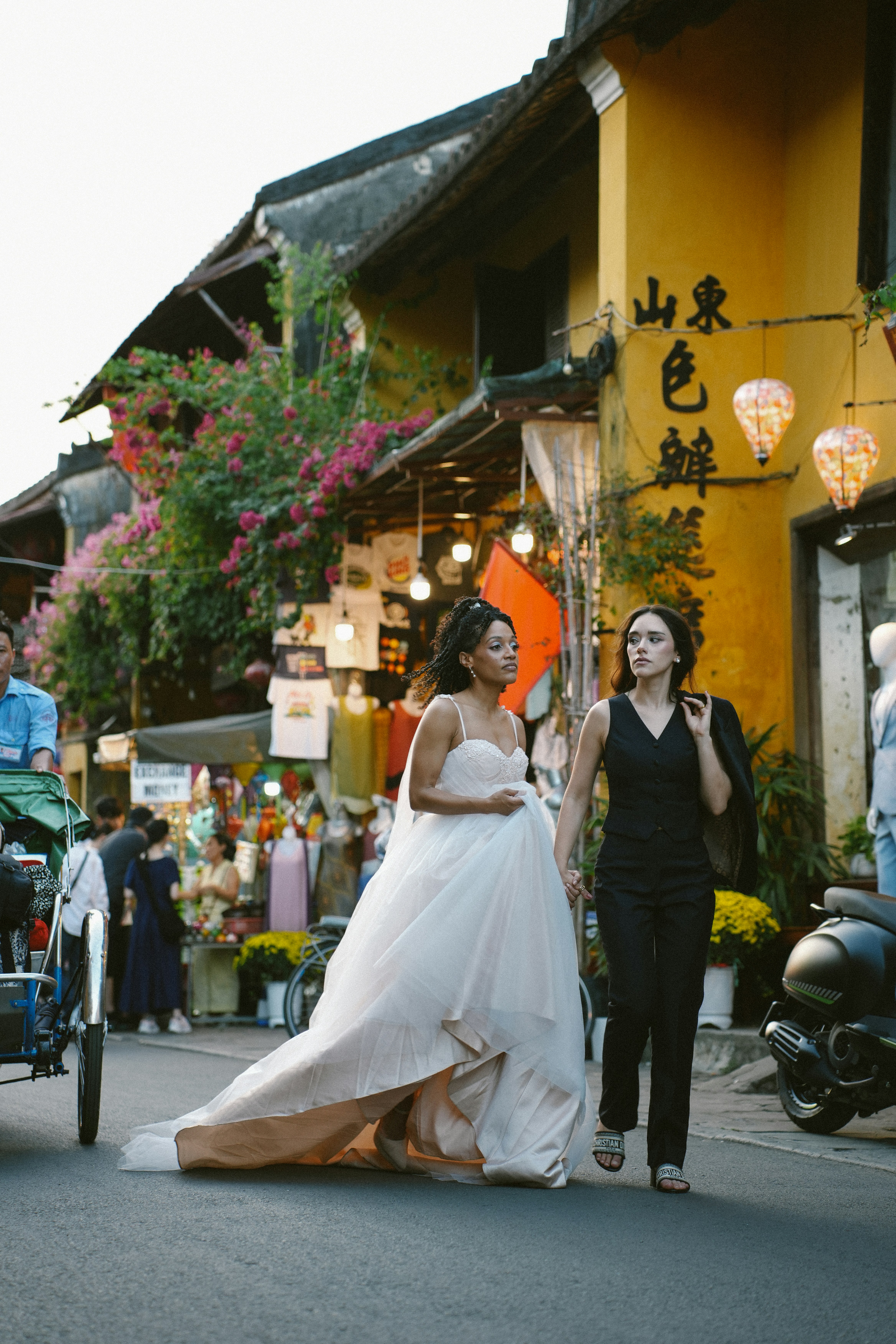 Bride and Friend Cross a Lantern-Lit Street in an Asian Market