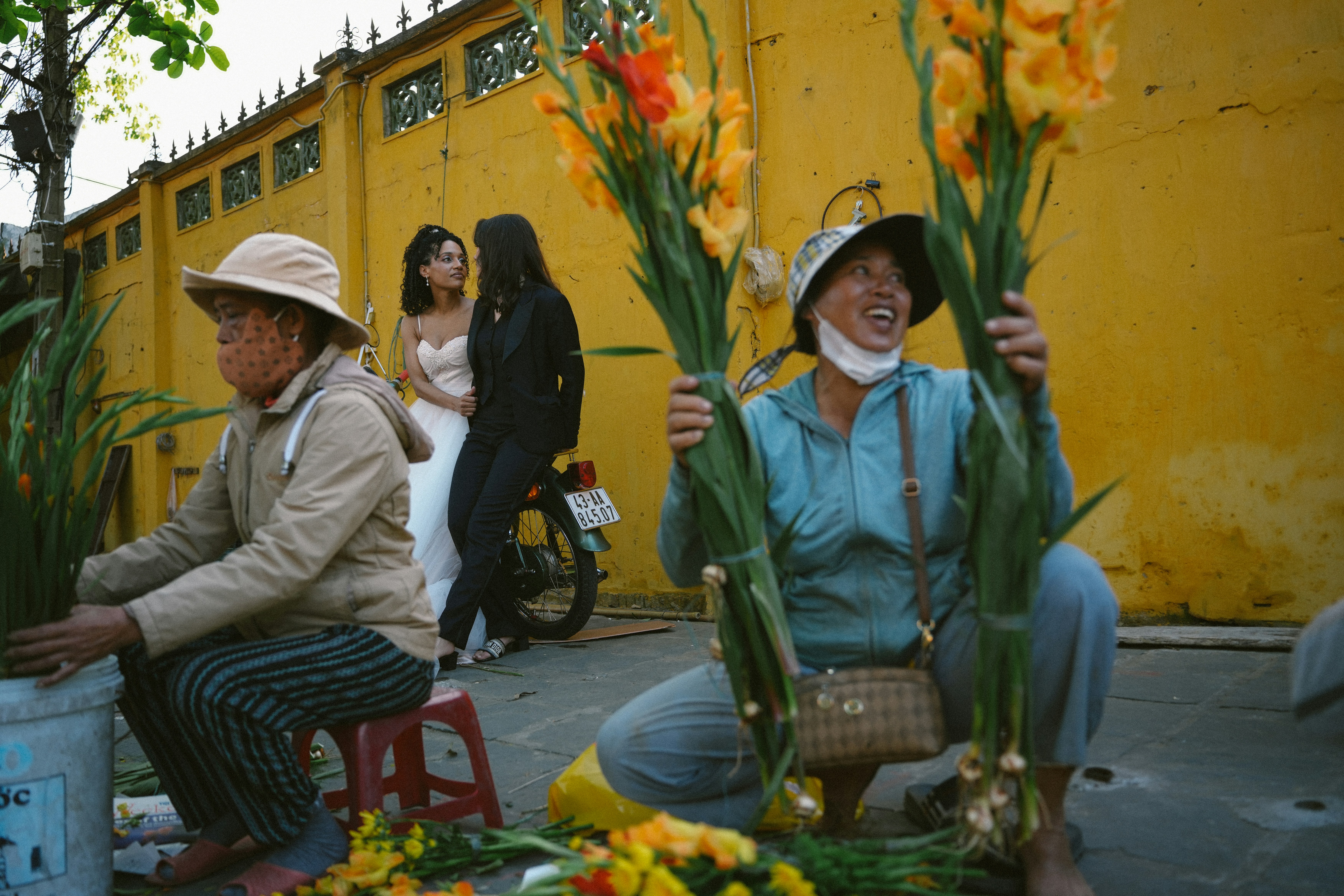Vendors with Floral Accents by a Sunlit Yellow Wall