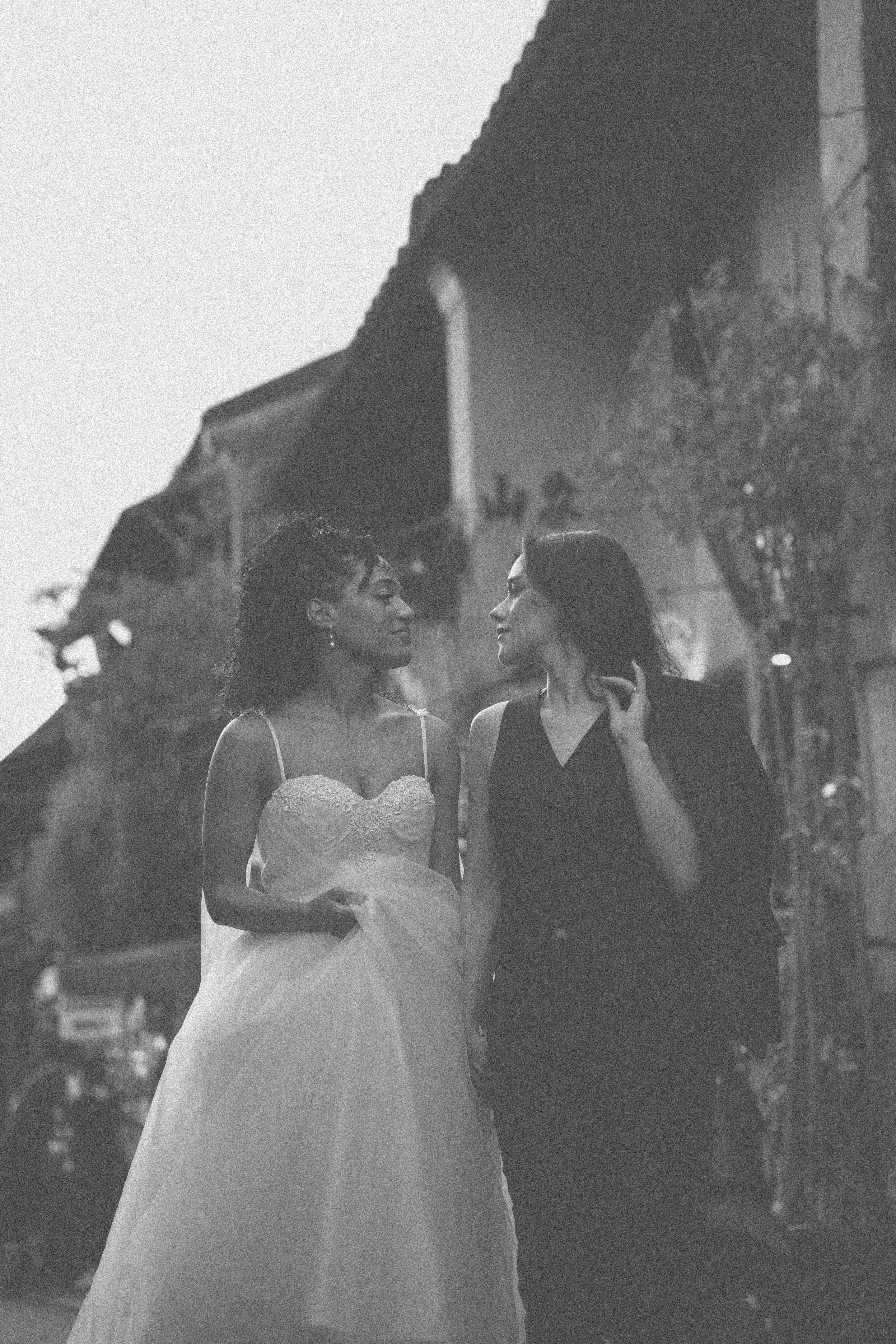 Two silhouettes in a grayscale moment: a bride and friend share a gaze on a city street