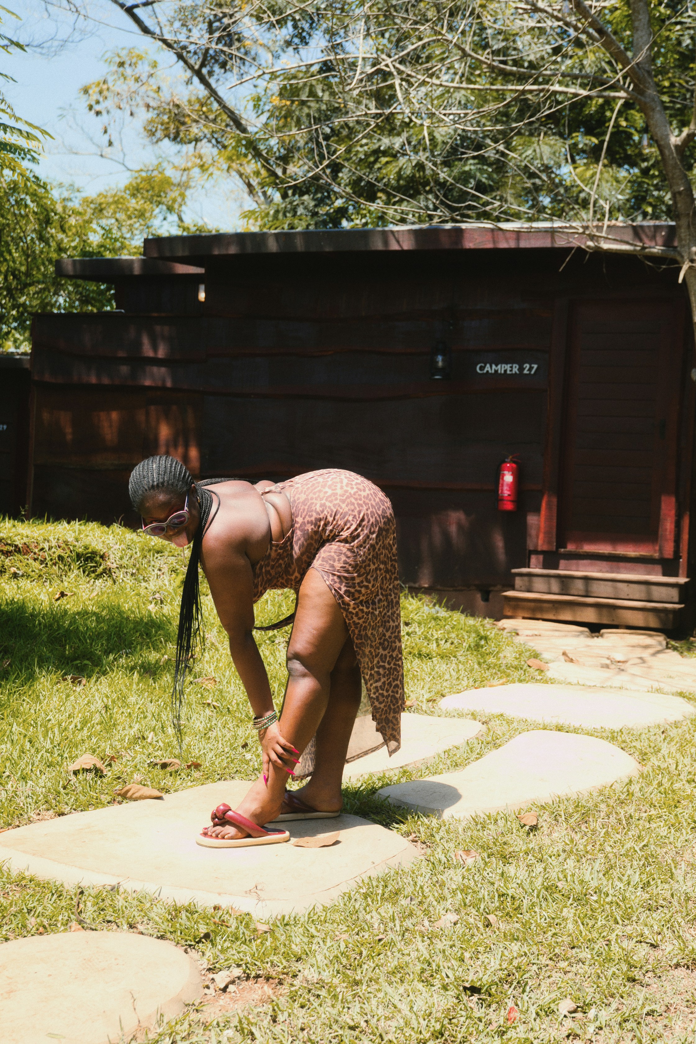 Bent Over in the Sun: A Woman Adjusts Her Sandals by a Rustic Cabin