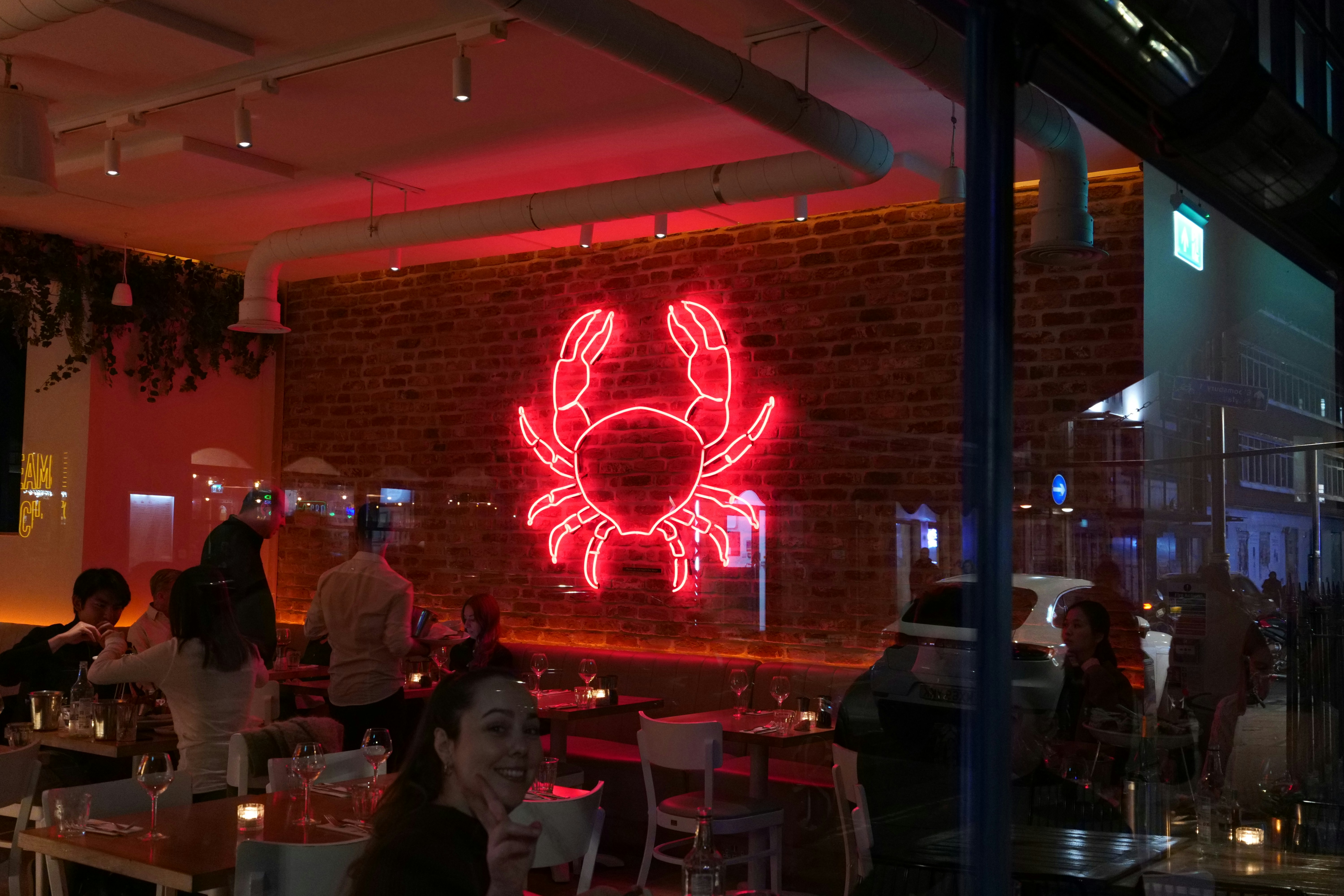 Neon Lobster Sign Illuminates a Social Night at the Brick-Walled Café