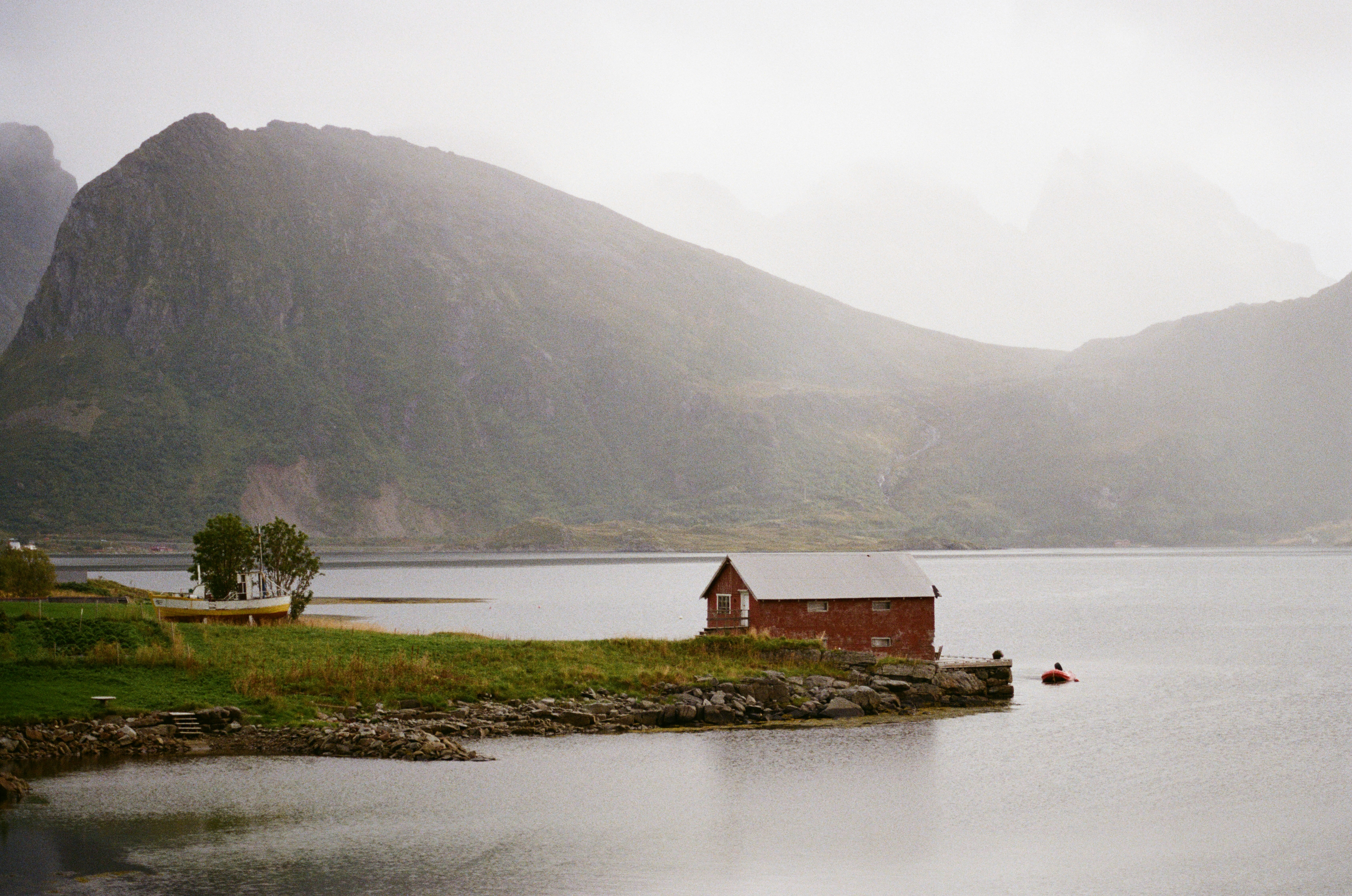 Red-roofed boathouse on a quiet fjord edge beneath misty mountains