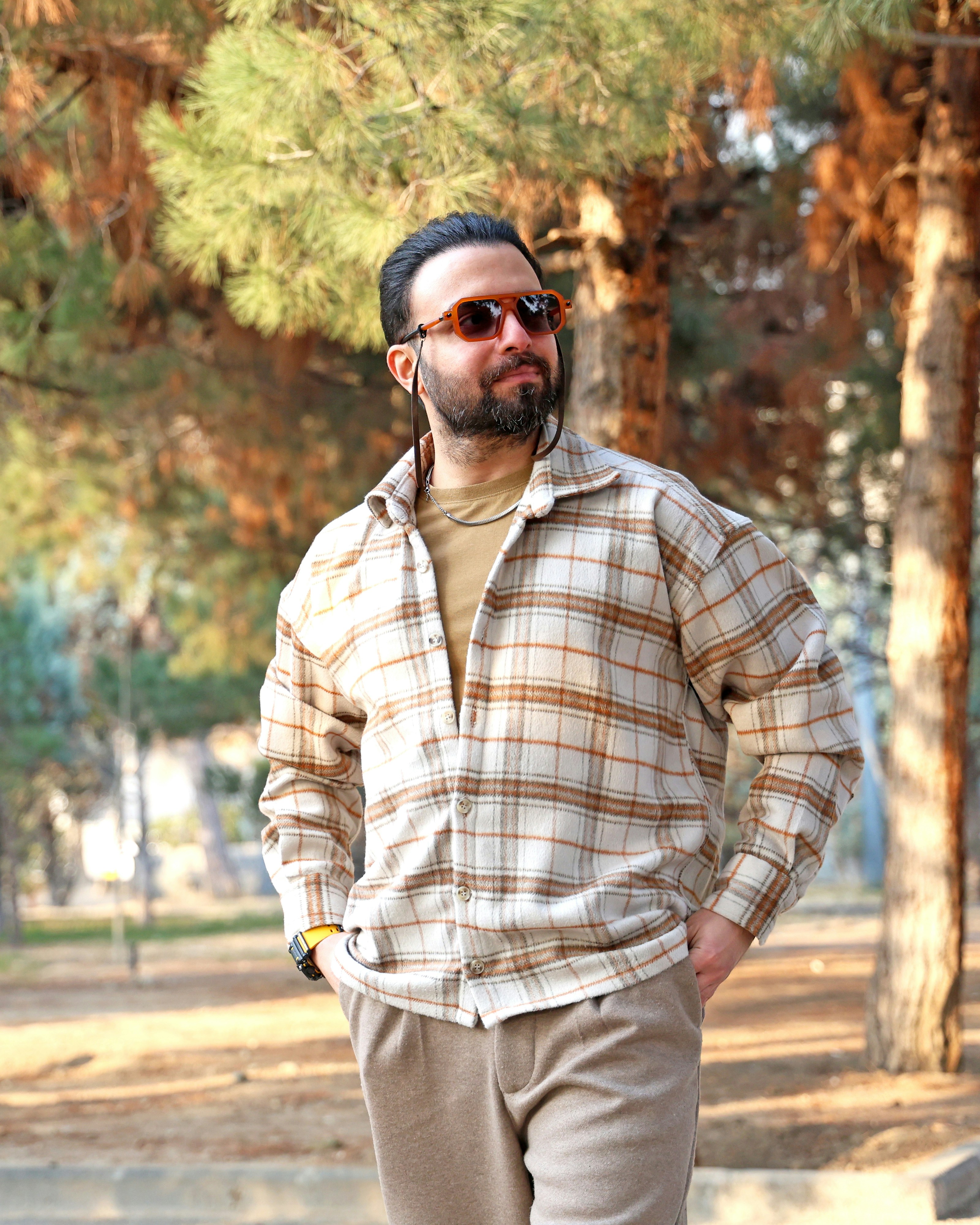 A man in plaid outdoors, shaded by pines, confident in the park