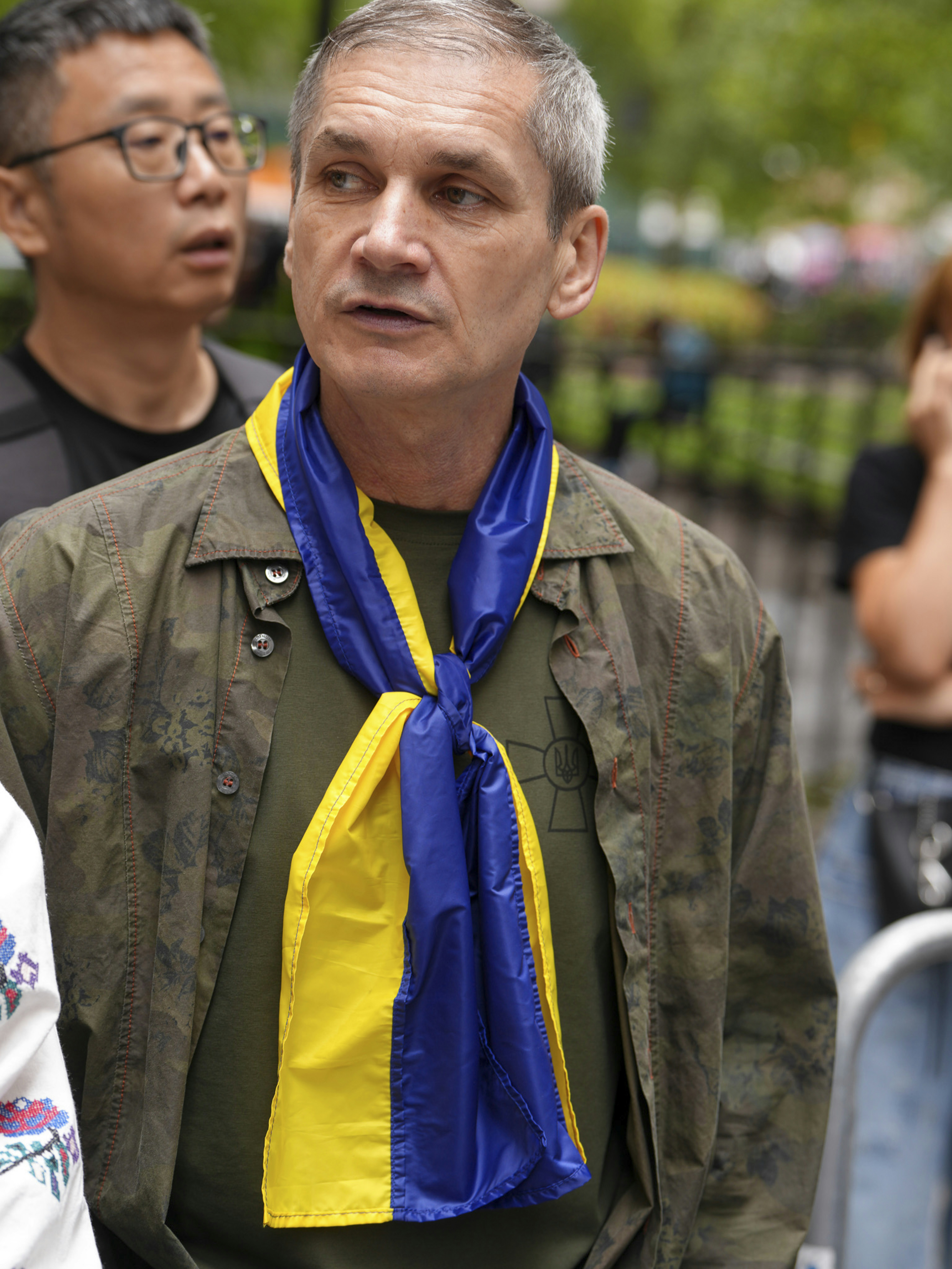 A Ukrainian rally unfolds in downtown Manhattan, where community members, NYC officials, and uniformed police gather in solidarity. A woman draped in a blue and yellow flag stands solemnly among the crowd, while a young attendee holds a folded Ukrainian flag during a formal civic ceremony. The event reflects unity, patriotism, and public support for Ukraine in the heart of New York City. Captured by Olek Buzunov @buzunov.photoart, documenting moments of resilience and civic engagement.