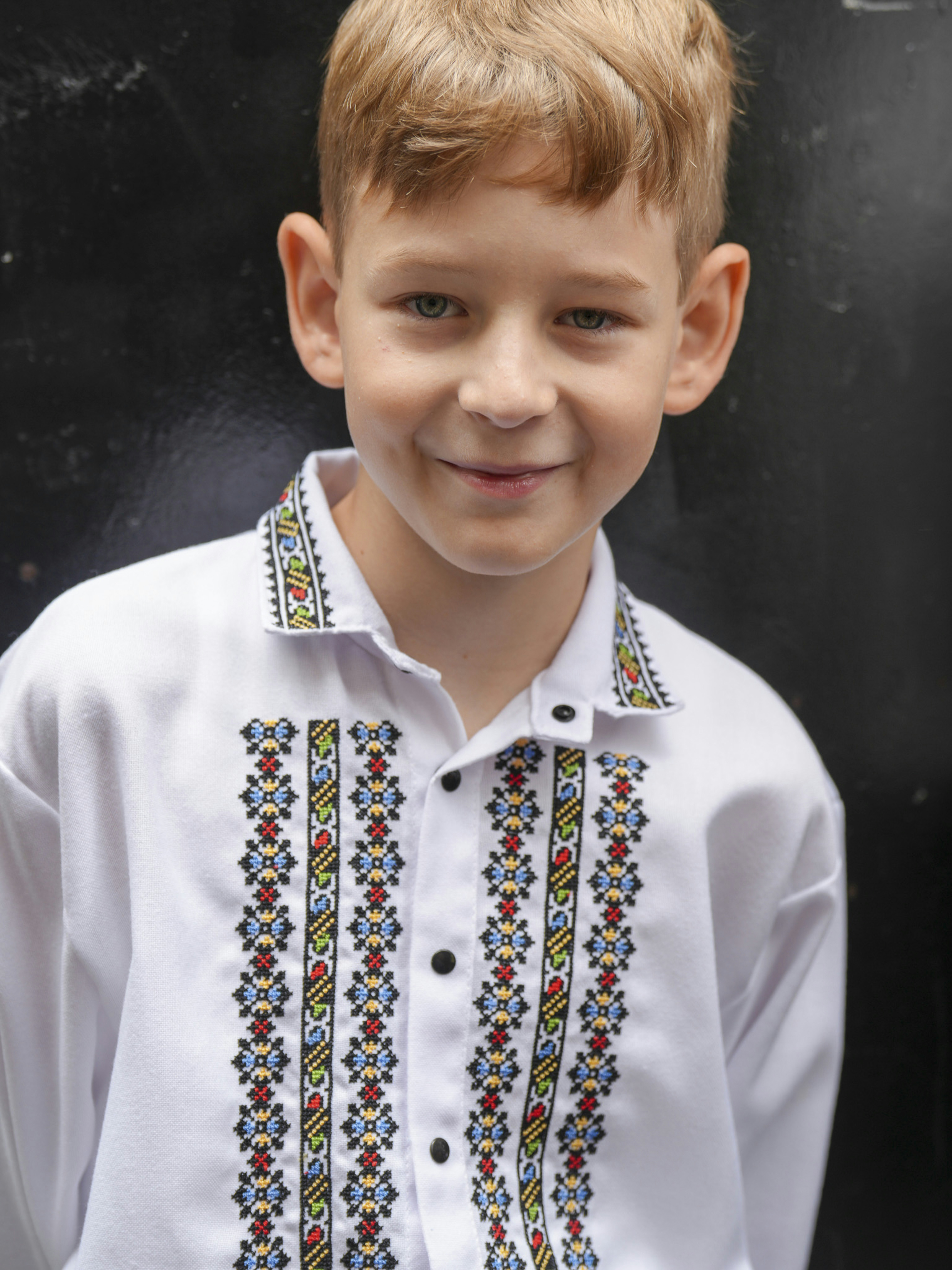 Portrait of a Smiling boy in a traditional embroidered shirt against a dark backdrop