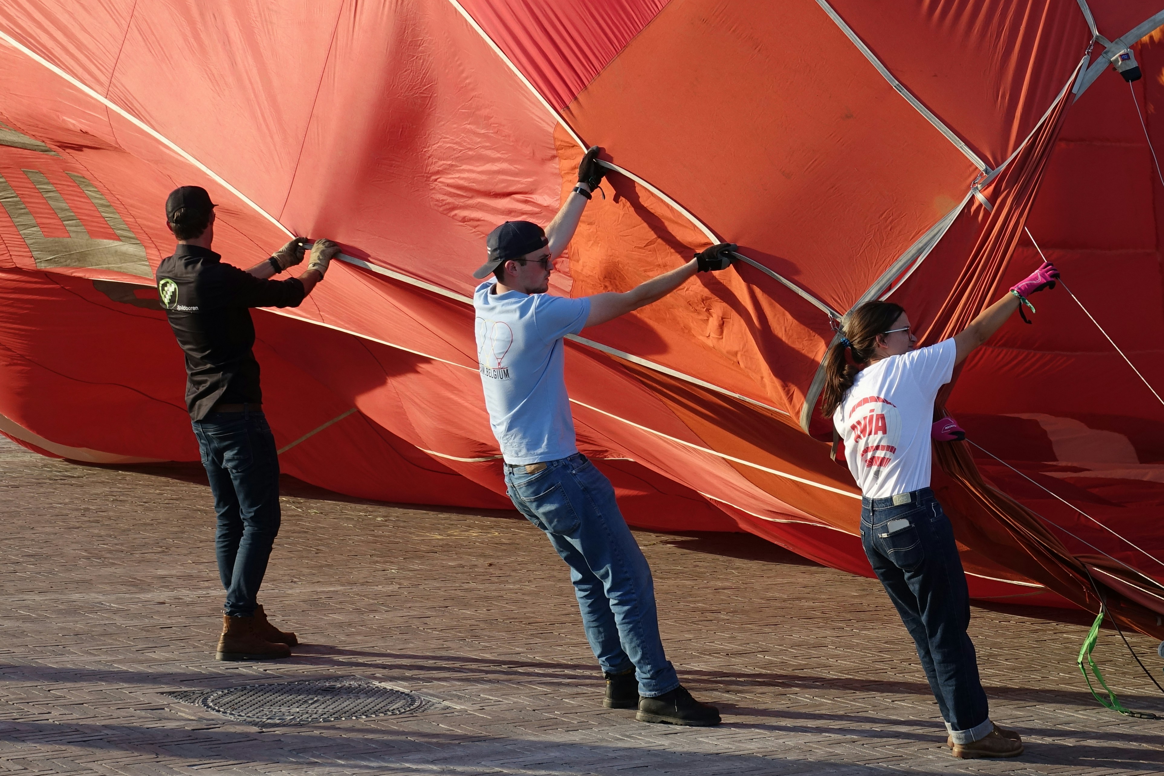 Teamwork Unfolding: Three Ground Crew Members Guiding a Balloon Split Between Sunlit Tarmac