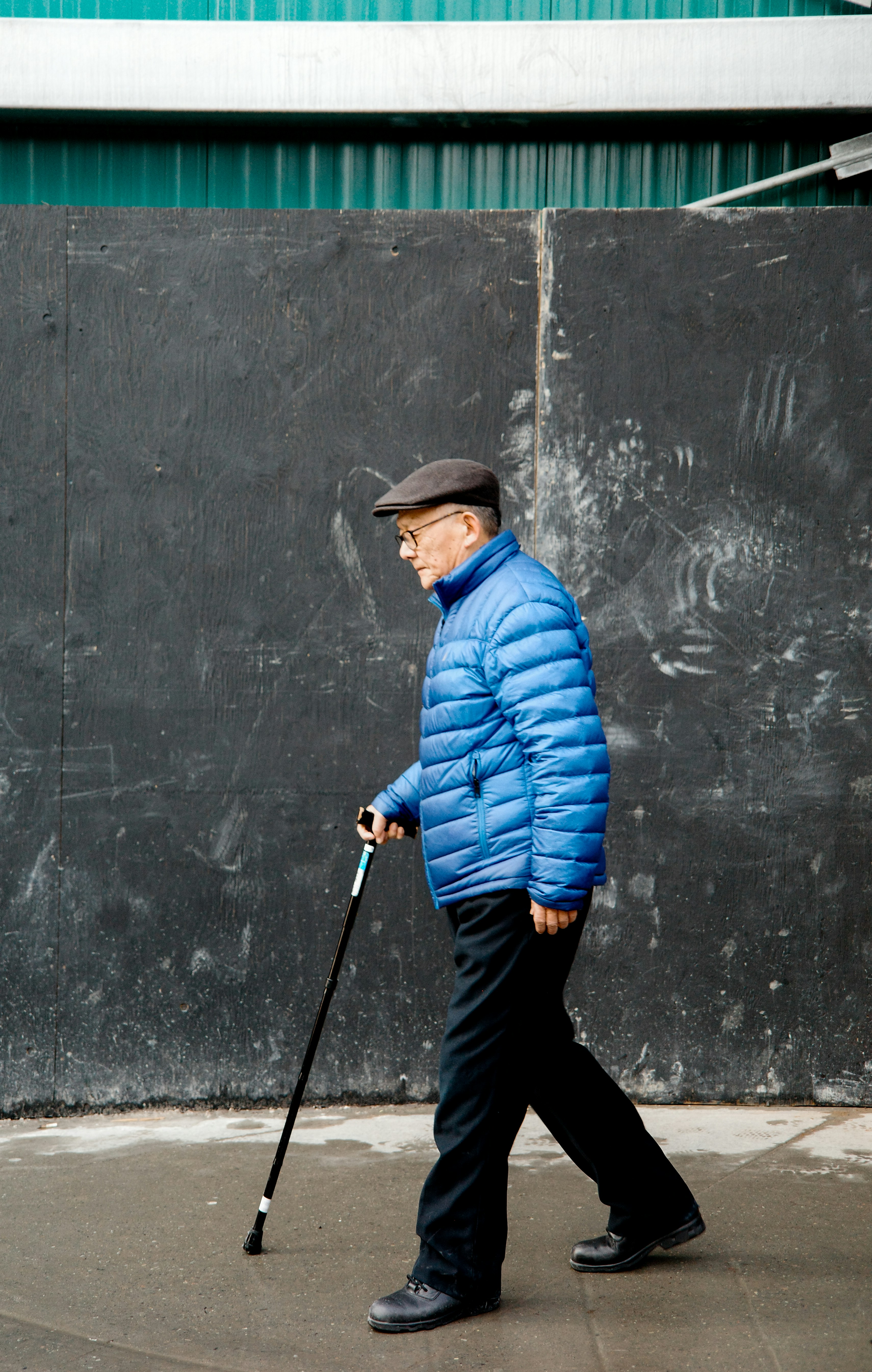 Blue-Insulated Walk: Elderly Man in Motion Against a Textured Wall