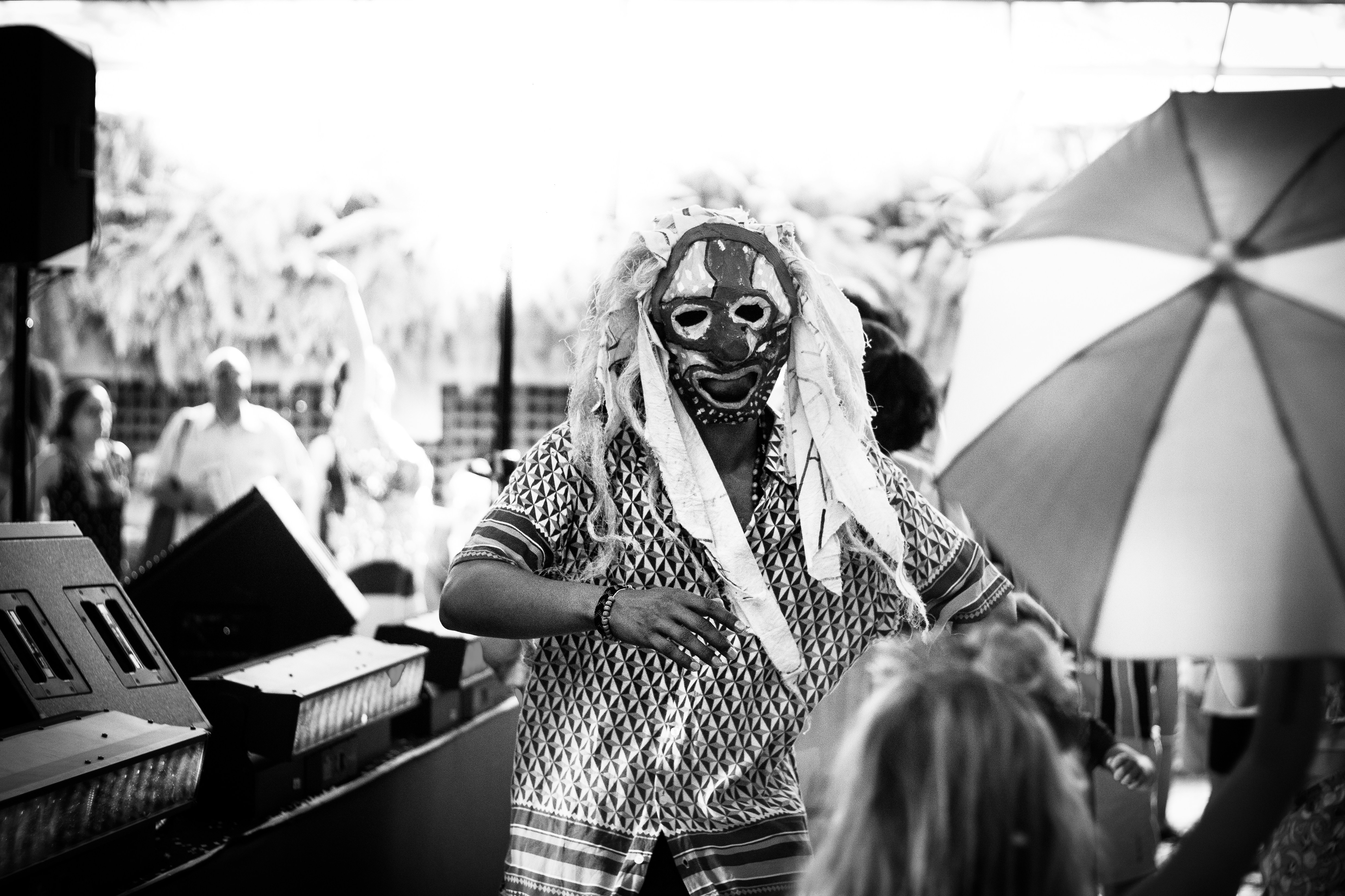 Masked performer commands the sunlit stage at a lively outdoor event