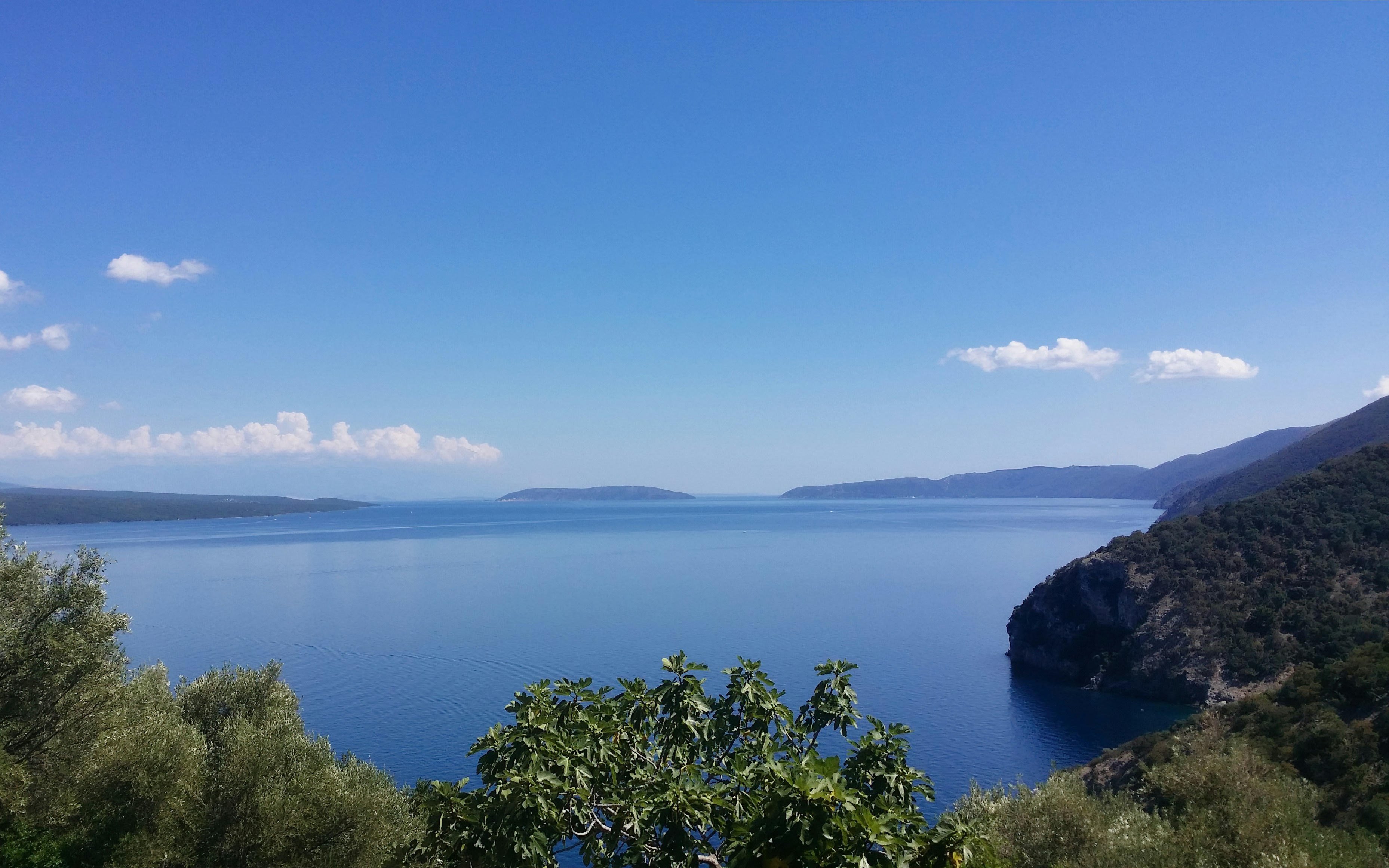 Vast blue lake surrounded by green hills under sky