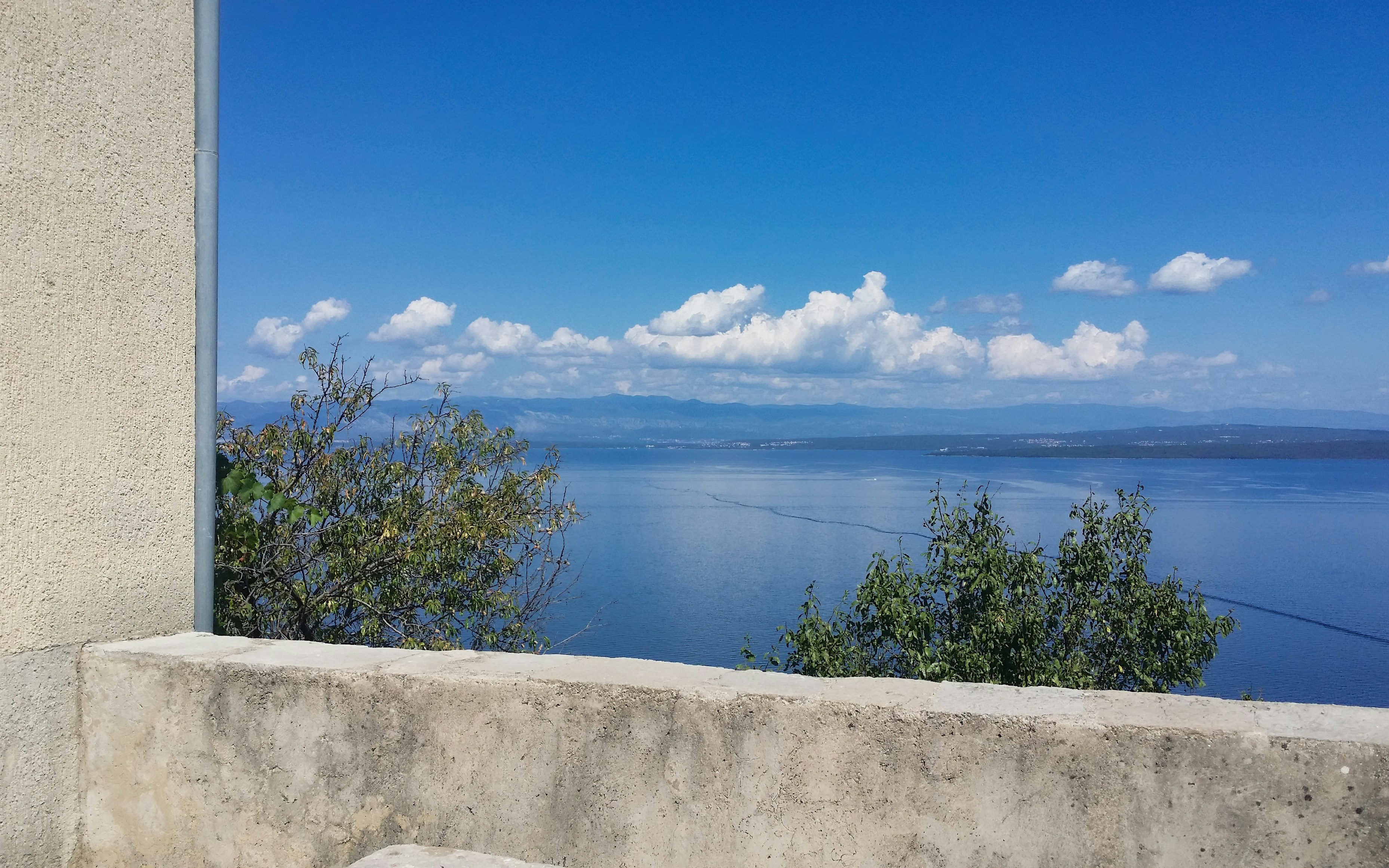Calm blue lake with distant mountains under a cloudy sky.