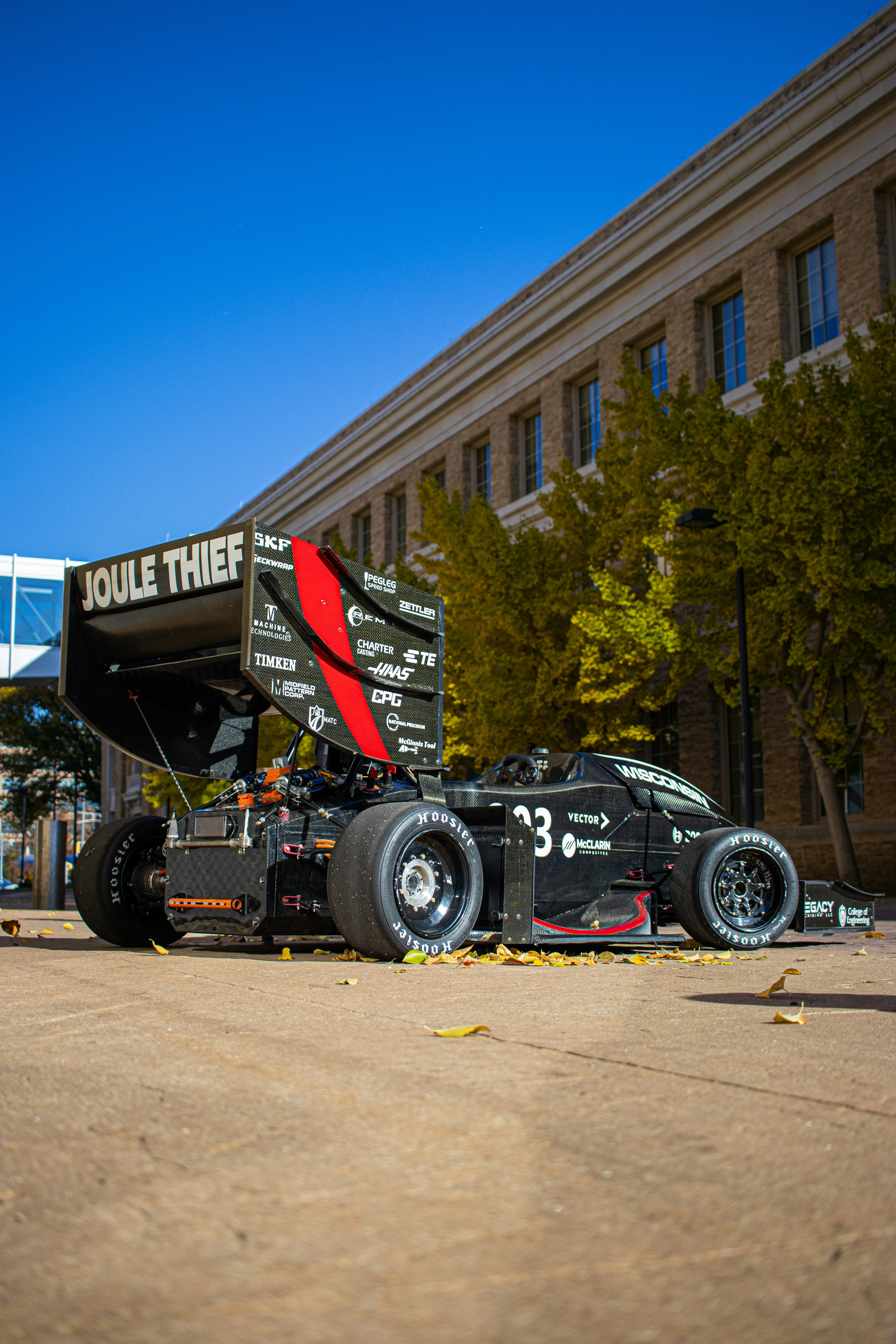 Black racecar on a sunlit plaza with a brick building backdrop