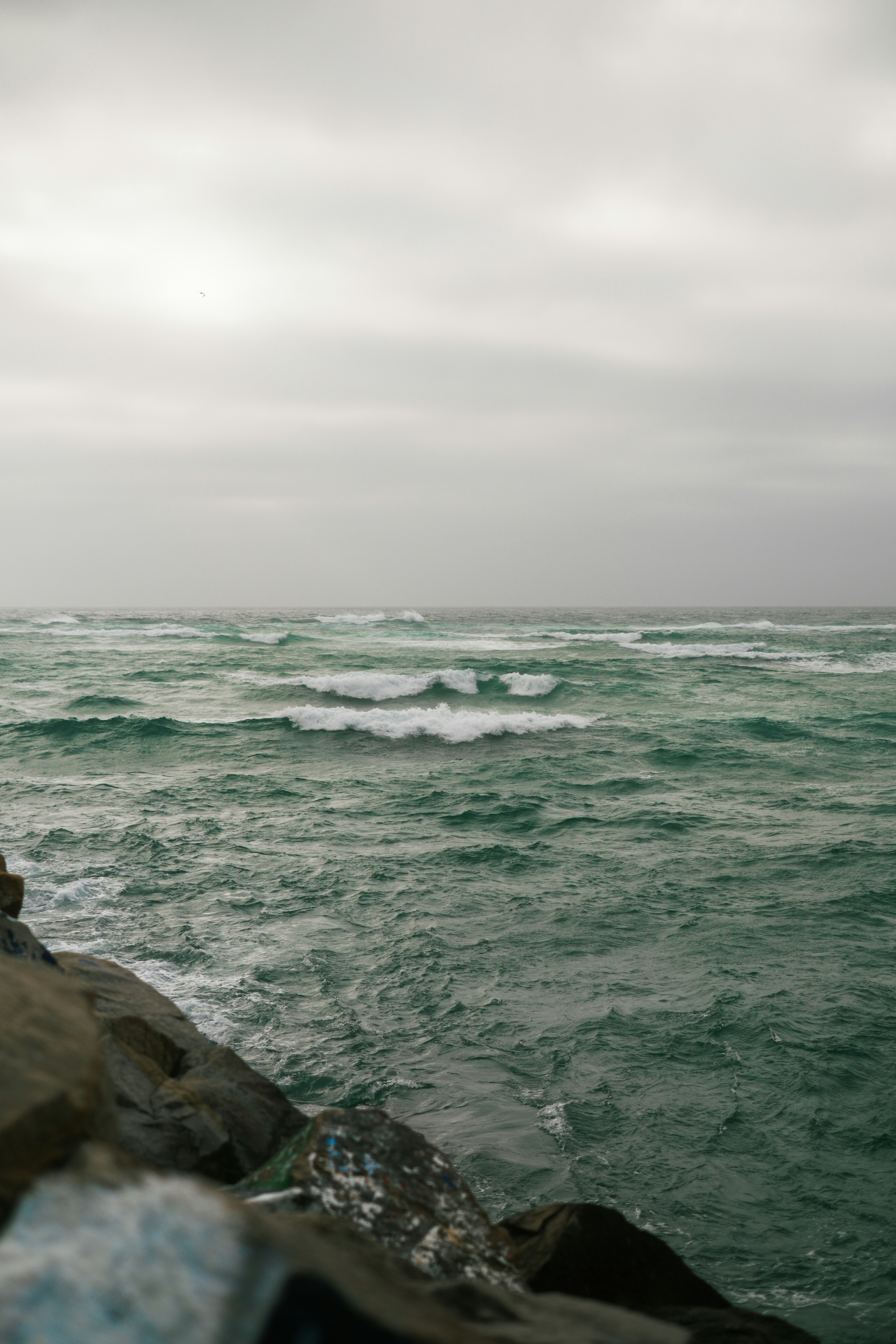 Sea's Edge: Waves Breaking Against a Quiet Jetty under Overcast Skies