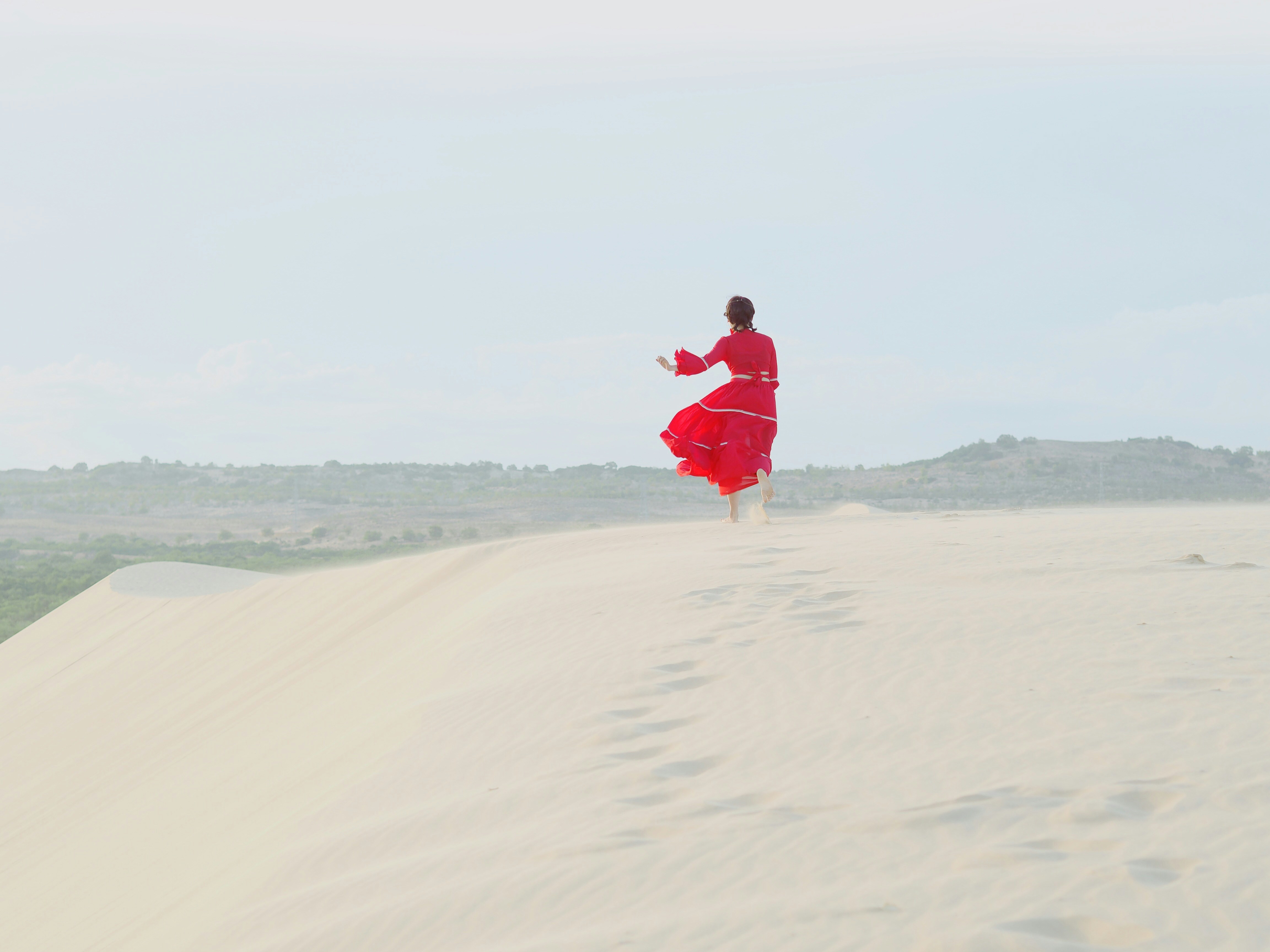Red-clad dancer atop a sunlit dune