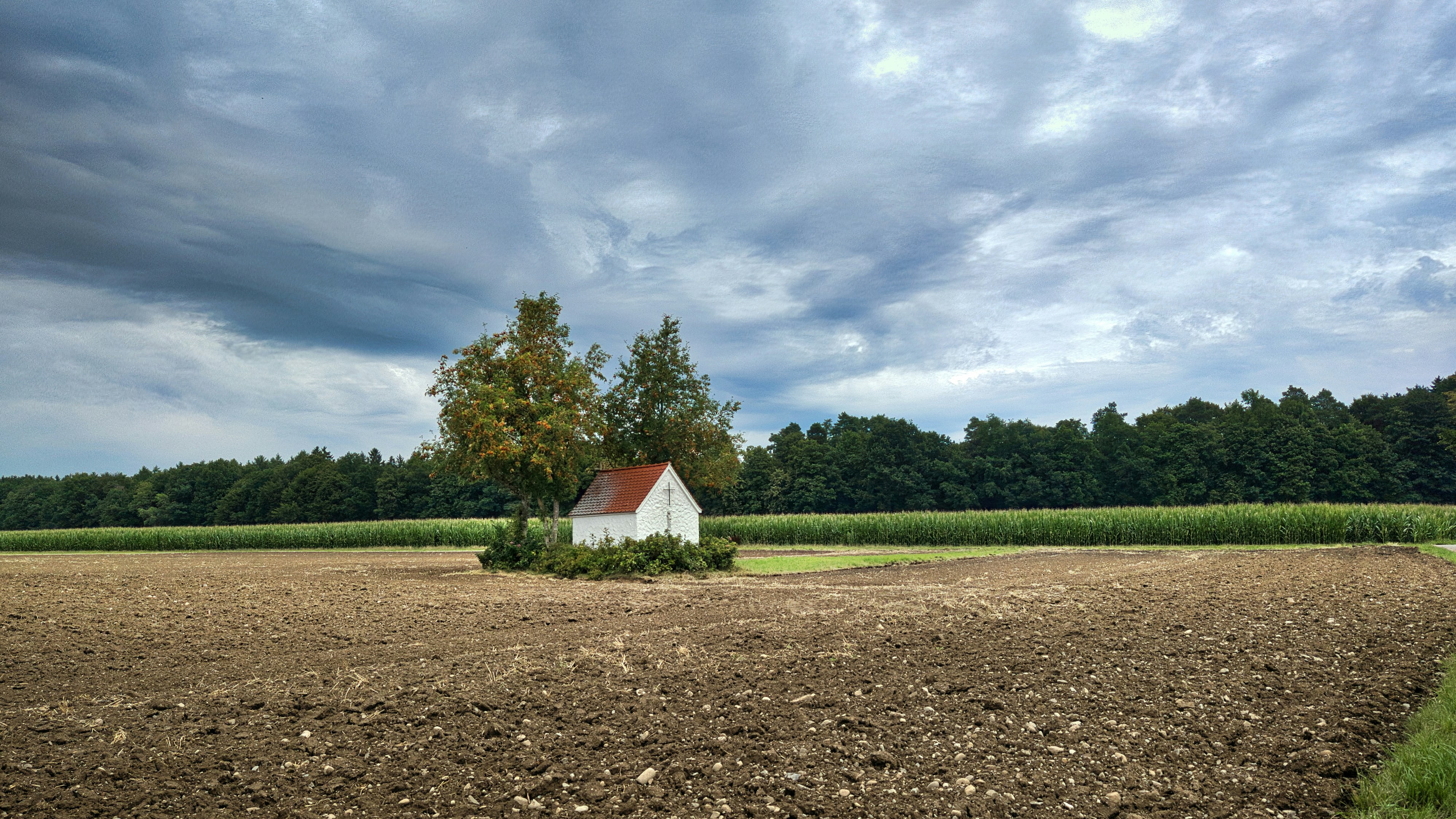 Small white building in a field under cloudy sky
