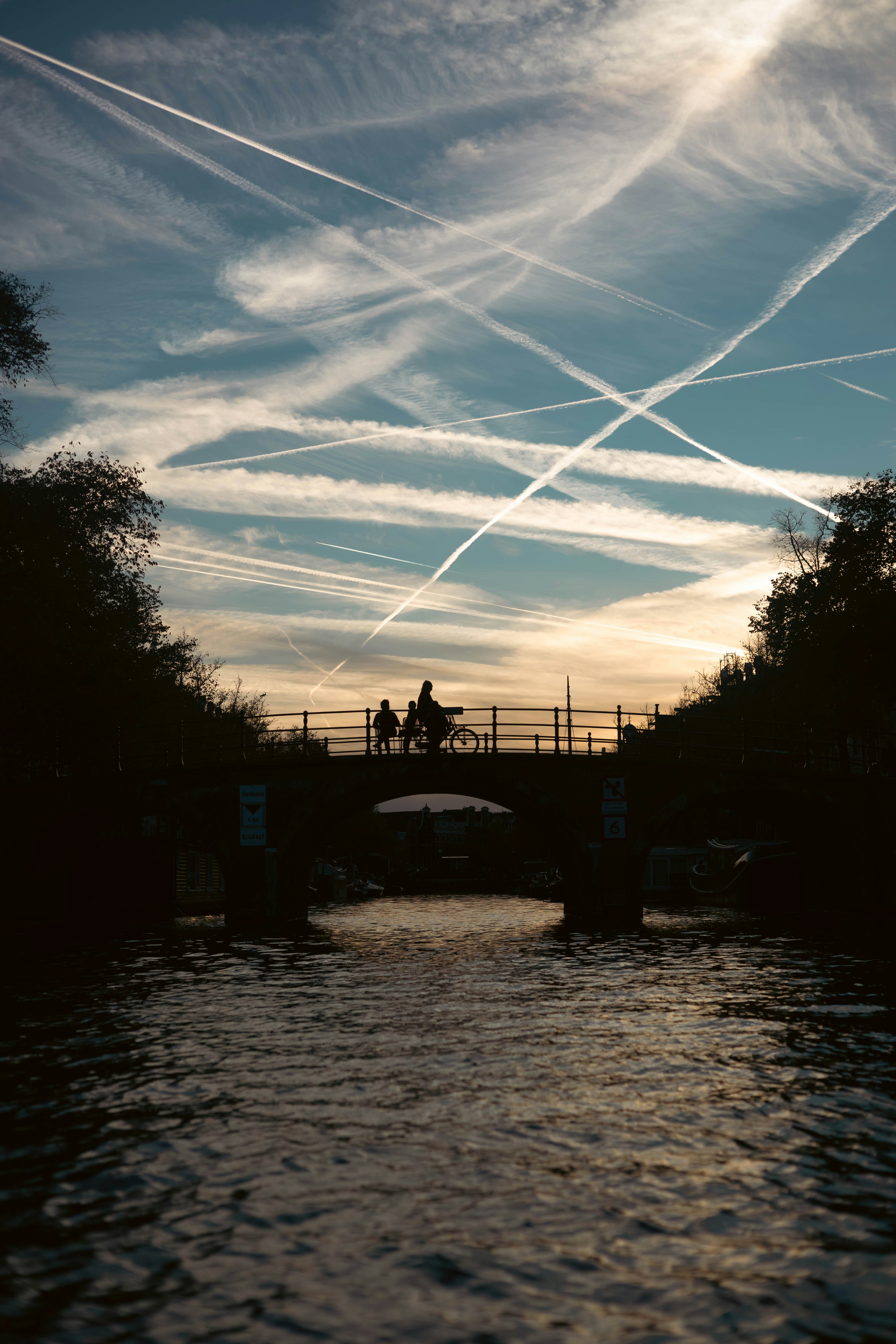 Silhouetted Pedestrians on a Bridge Beneath Sky-Willowed Contrails at Dusk