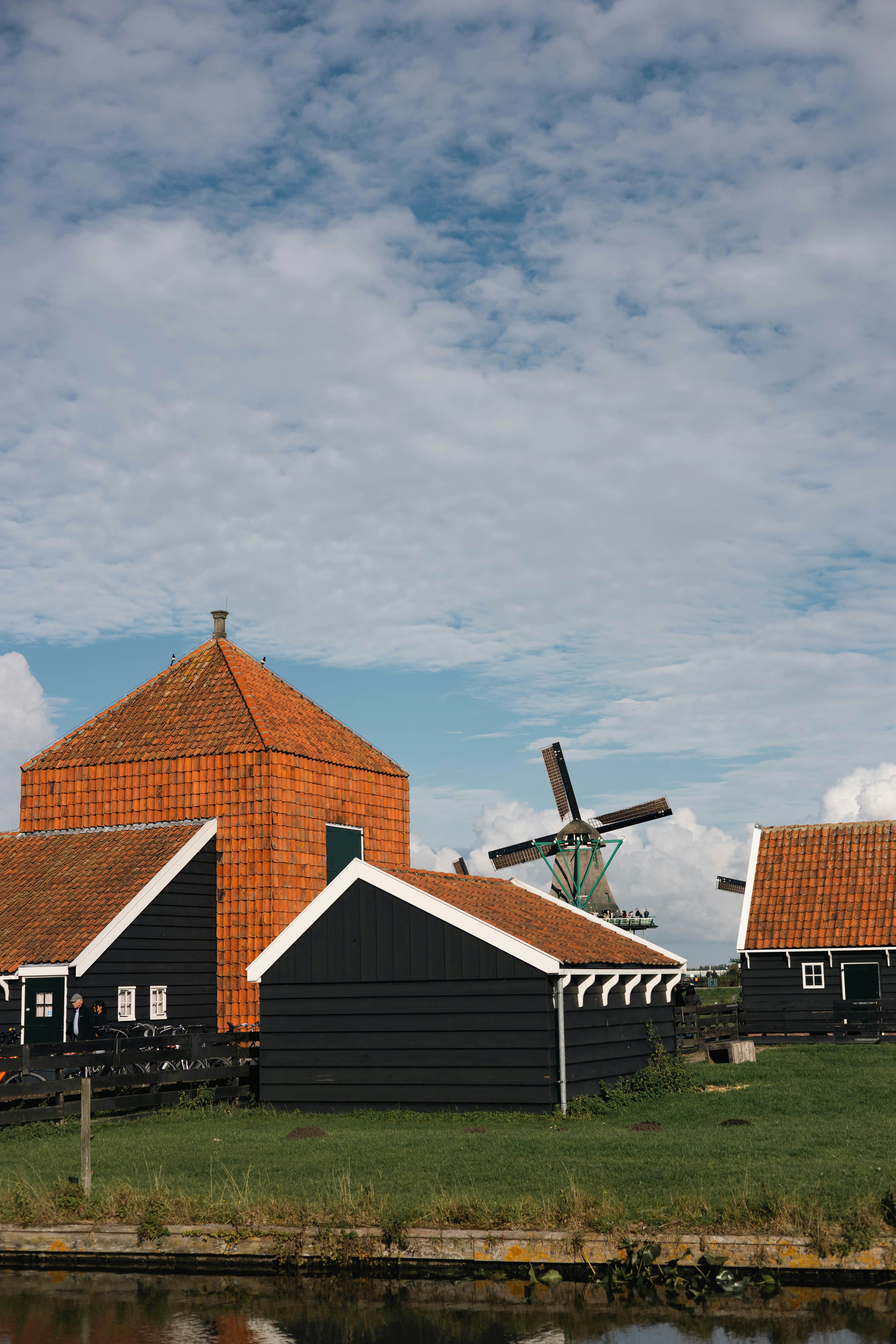 Row of black cottages with orange-tiled roofs beside a canal under a cloudy blue sky