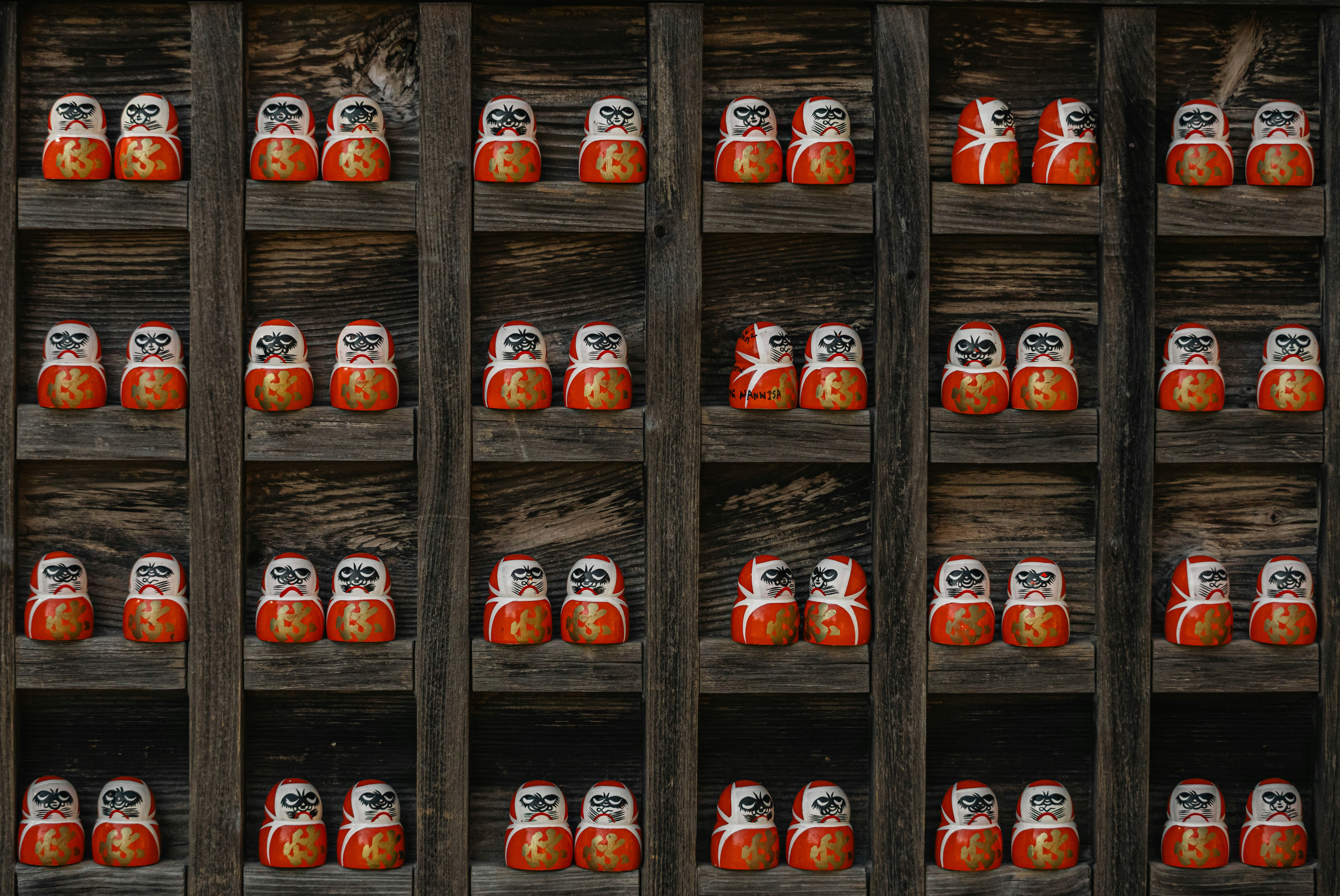 Rows of Orange Faces: Daruma Dolls Align in a Wooden Grid