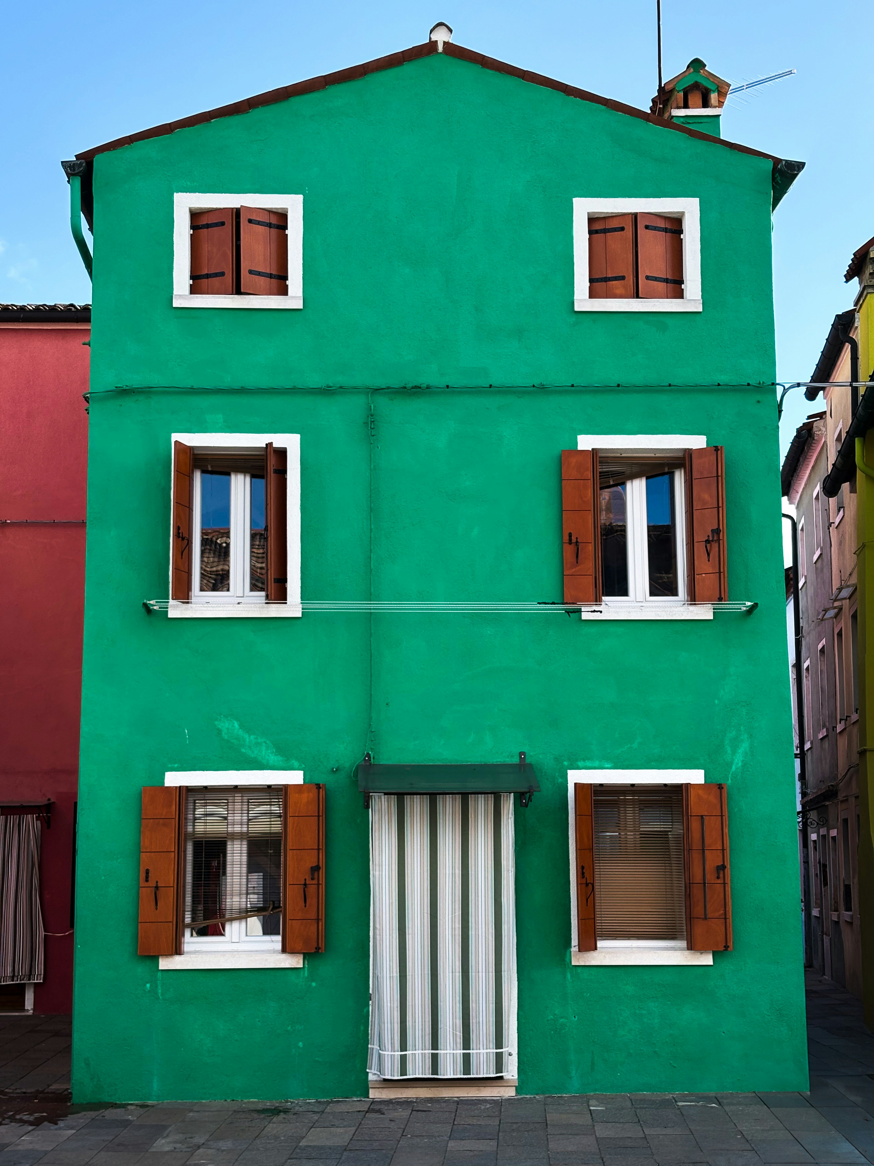 Emerald Facade: A Three-Story Green House with Wooden Shuttered Windows