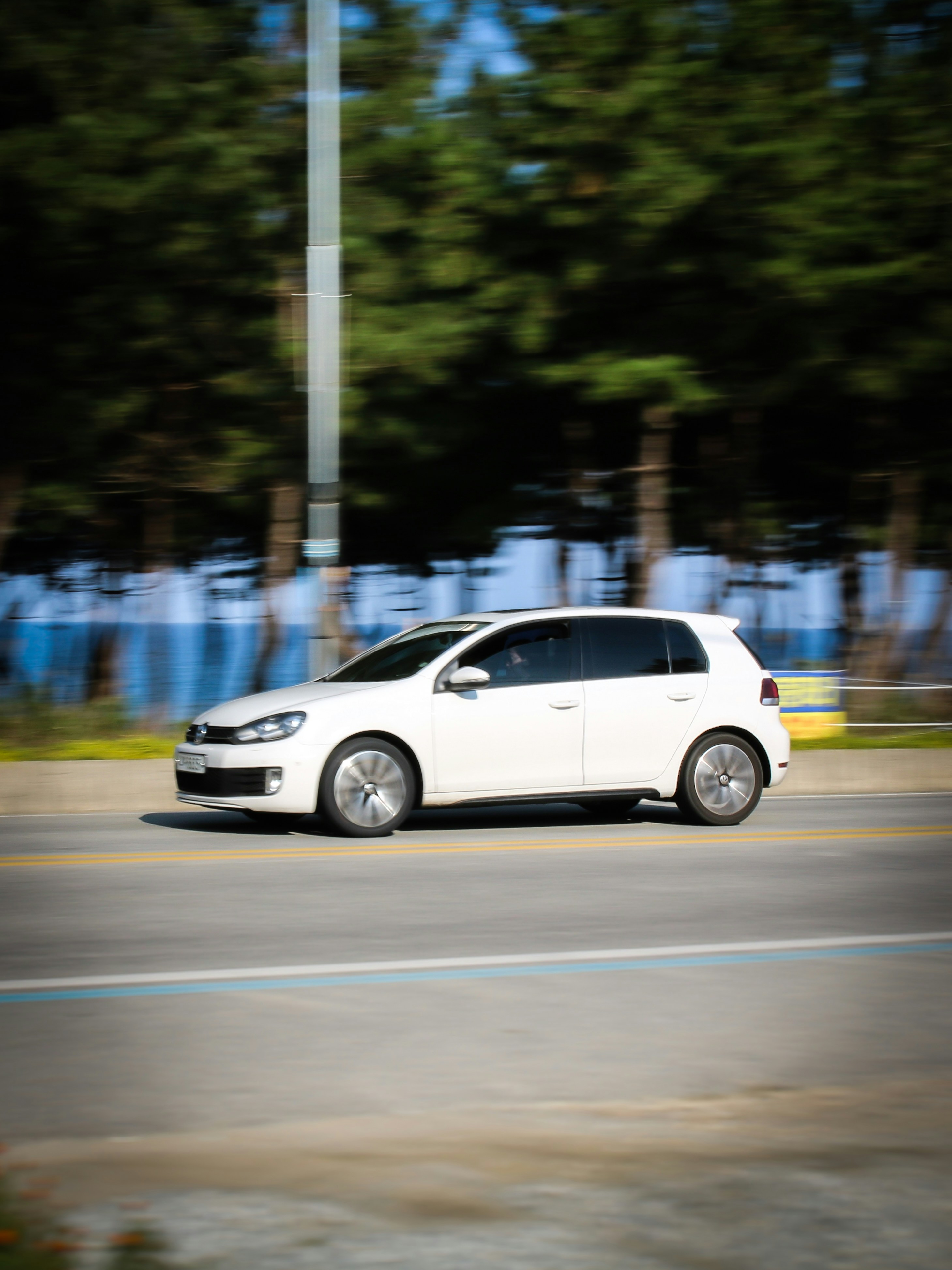 White hatchback in motion along a seaside road