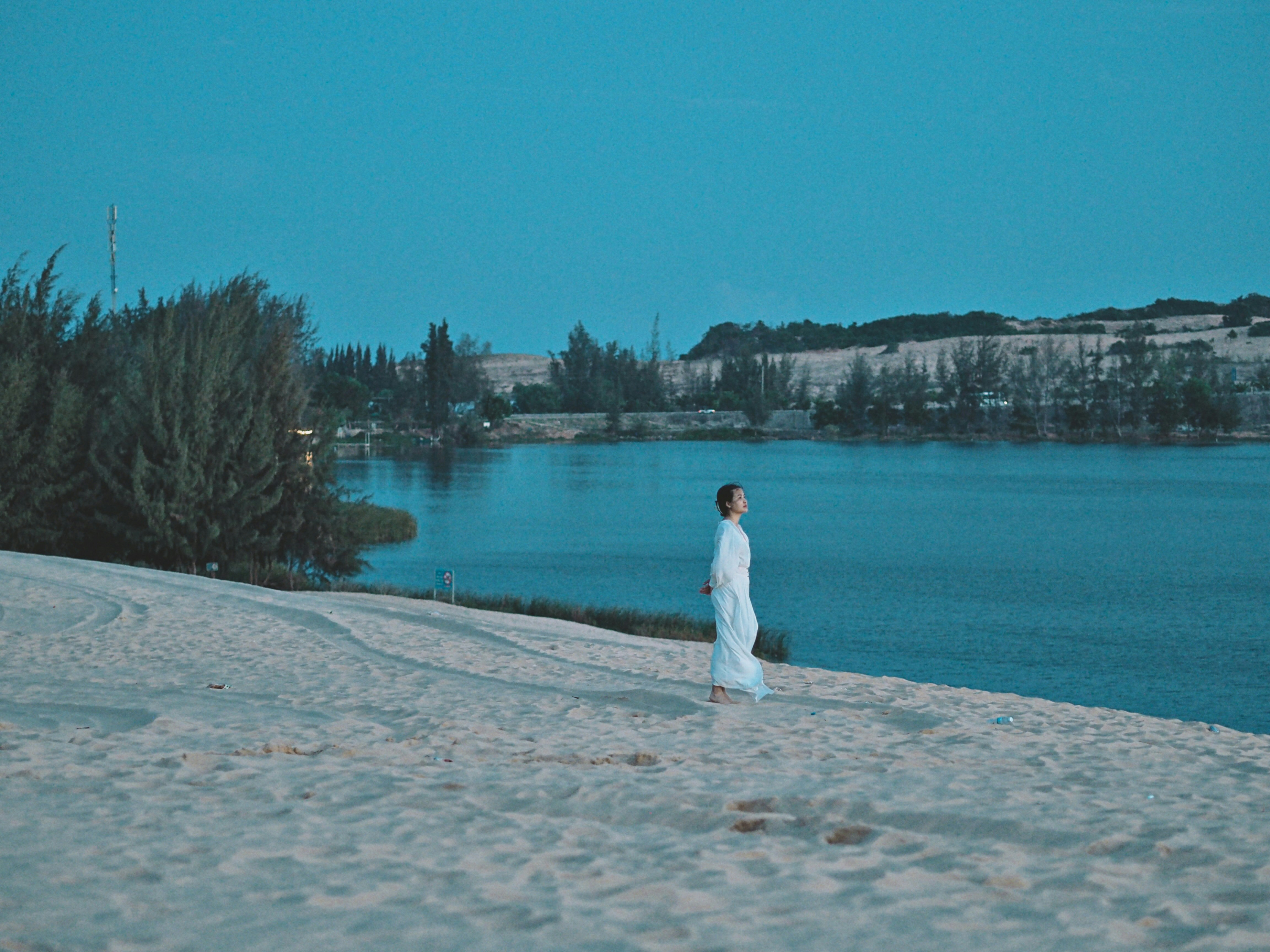 White-dressed figure on a tranquil shoreline under a turquoise sky
