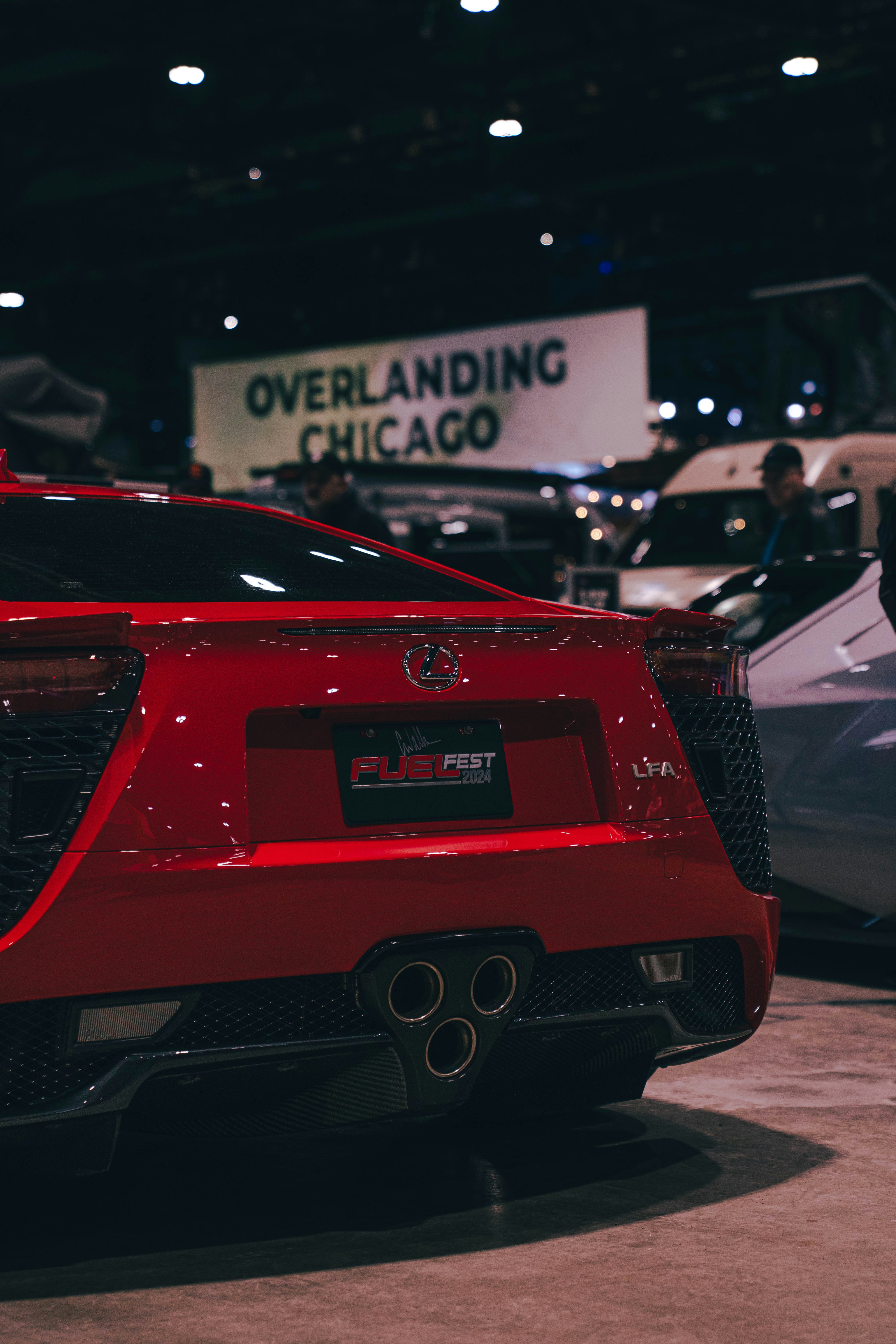 Rear view of a red Lexus at an auto show with a 'FUEL FEST' plate