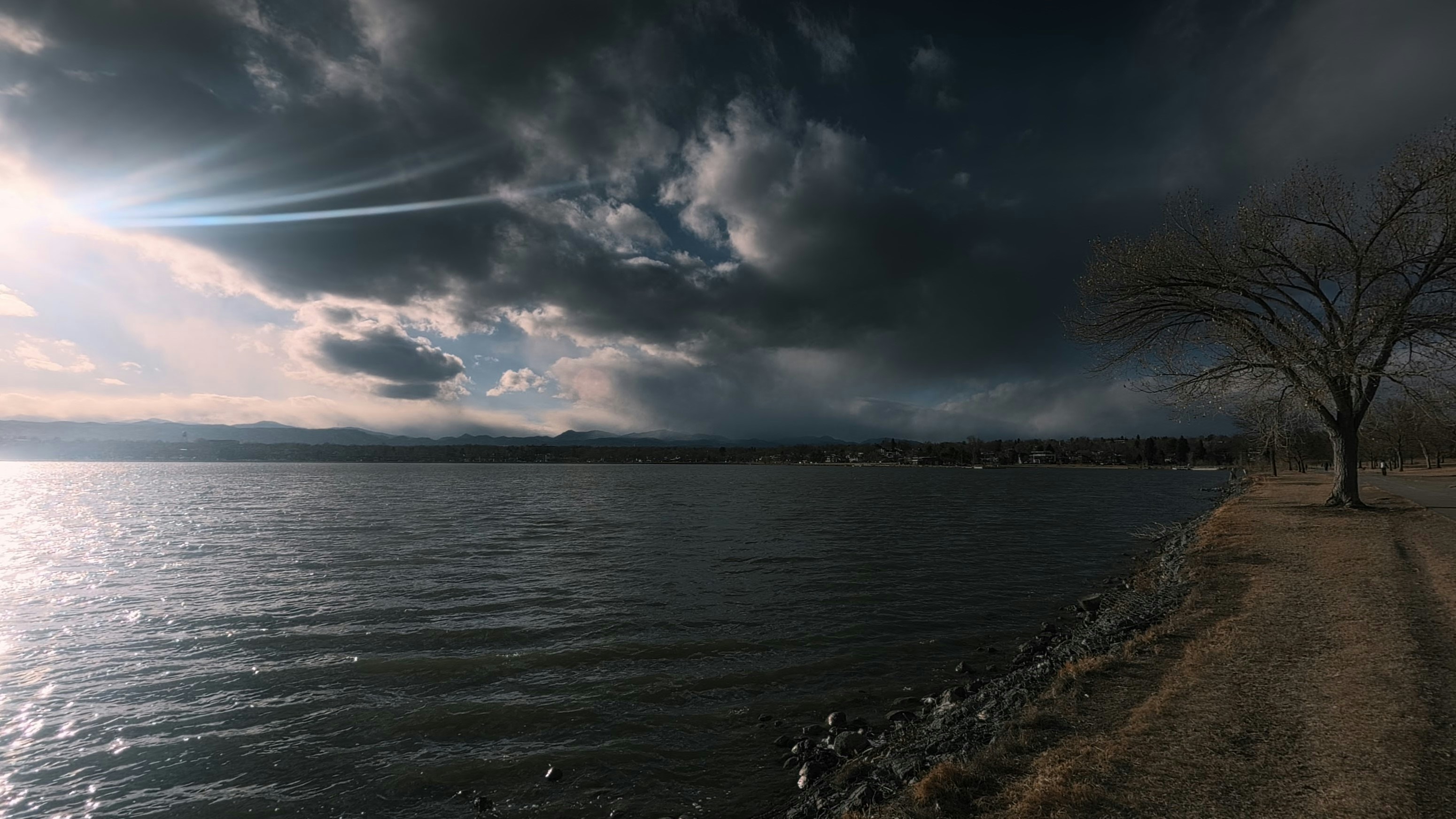 Stormy sky over a calm lake with a lone tree.