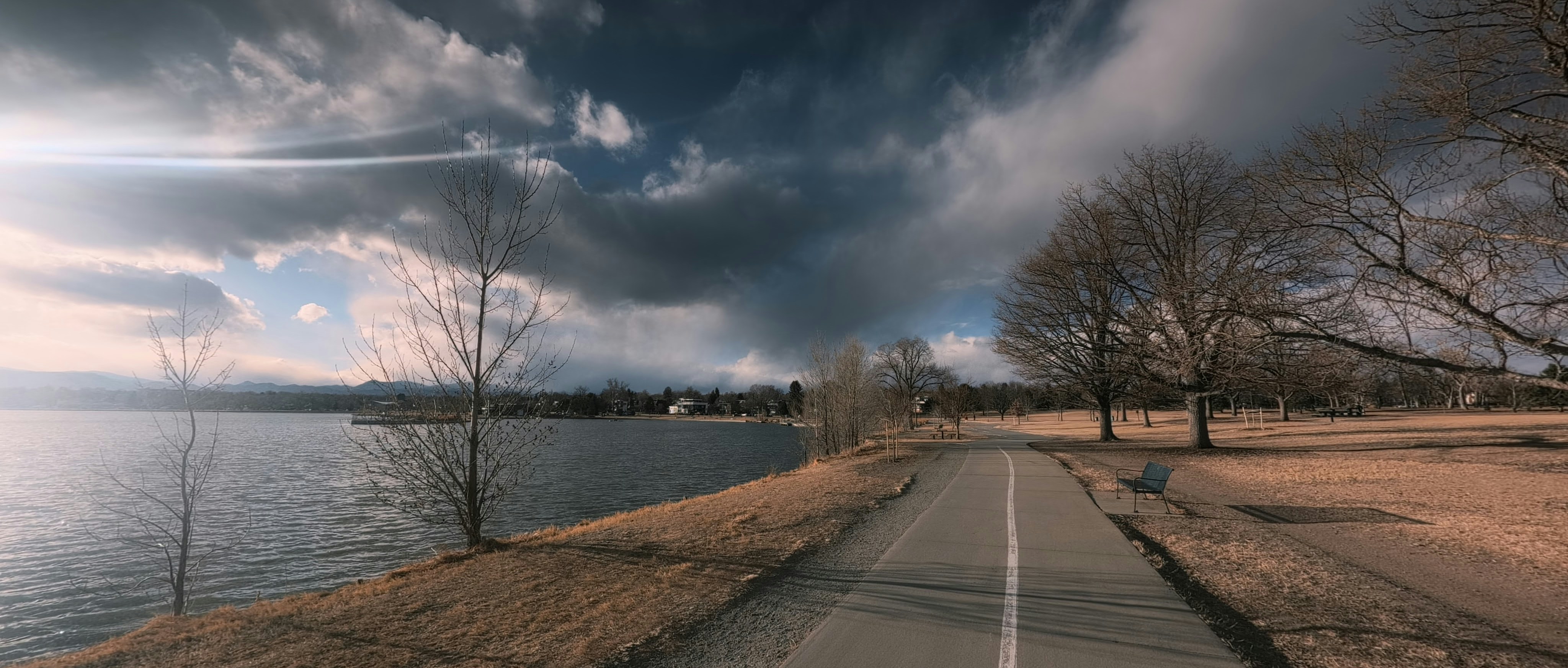 A paved path alongside a lake under stormy skies.