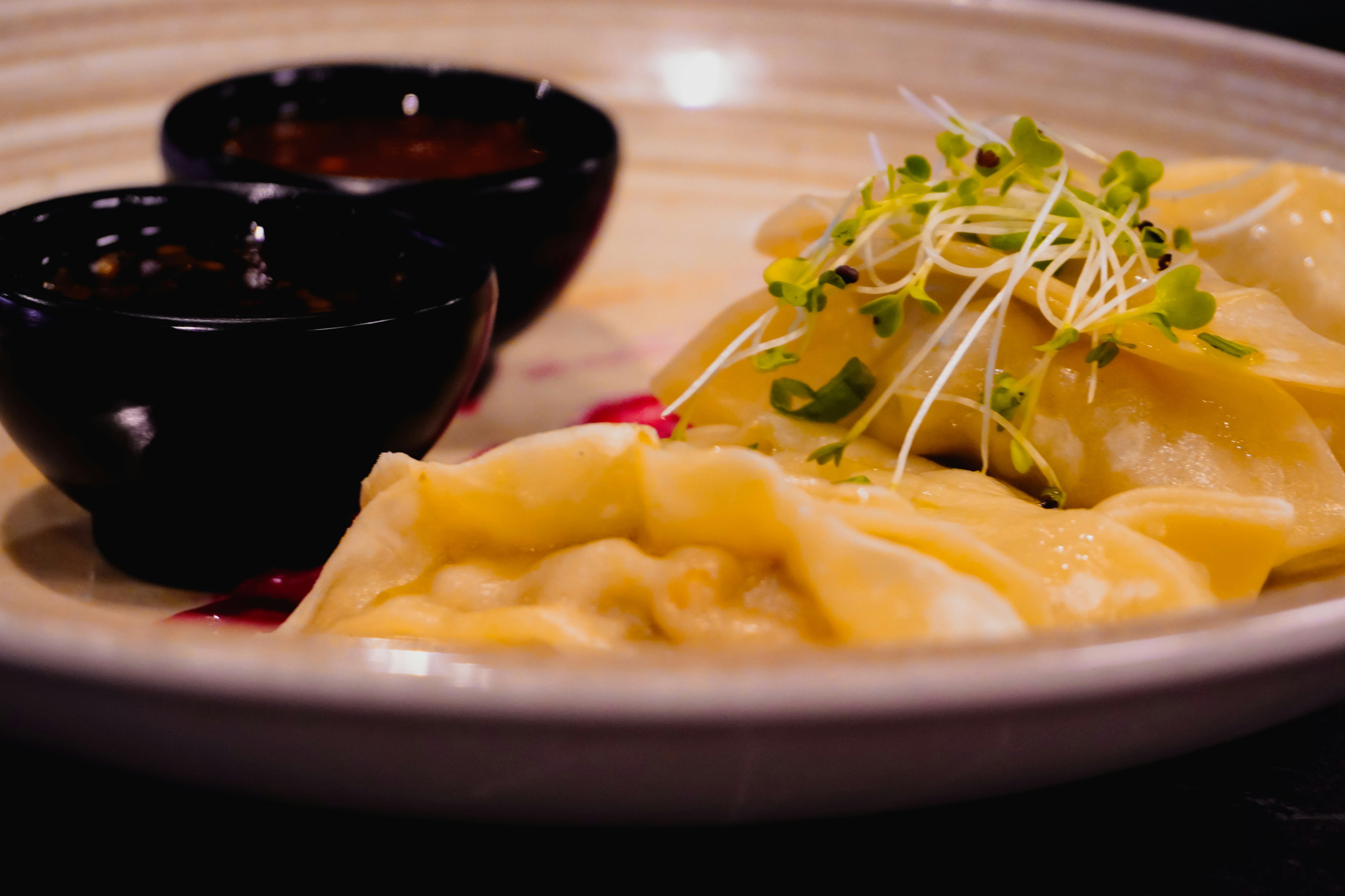 Dumplings with microgreens and dipping sauce on a shallow plate