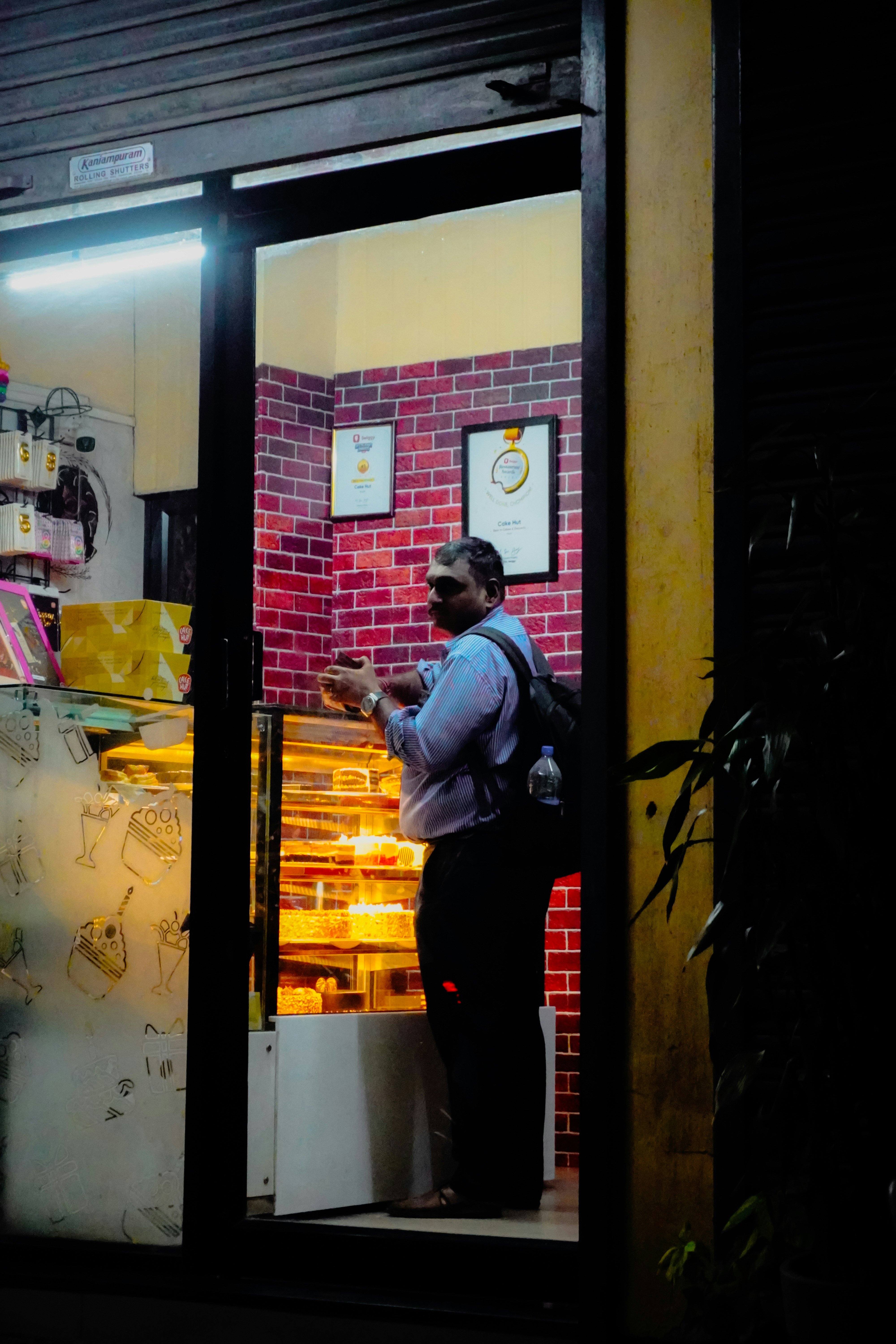 Night Sale: A man at a bakery counter framed through a glass storefront