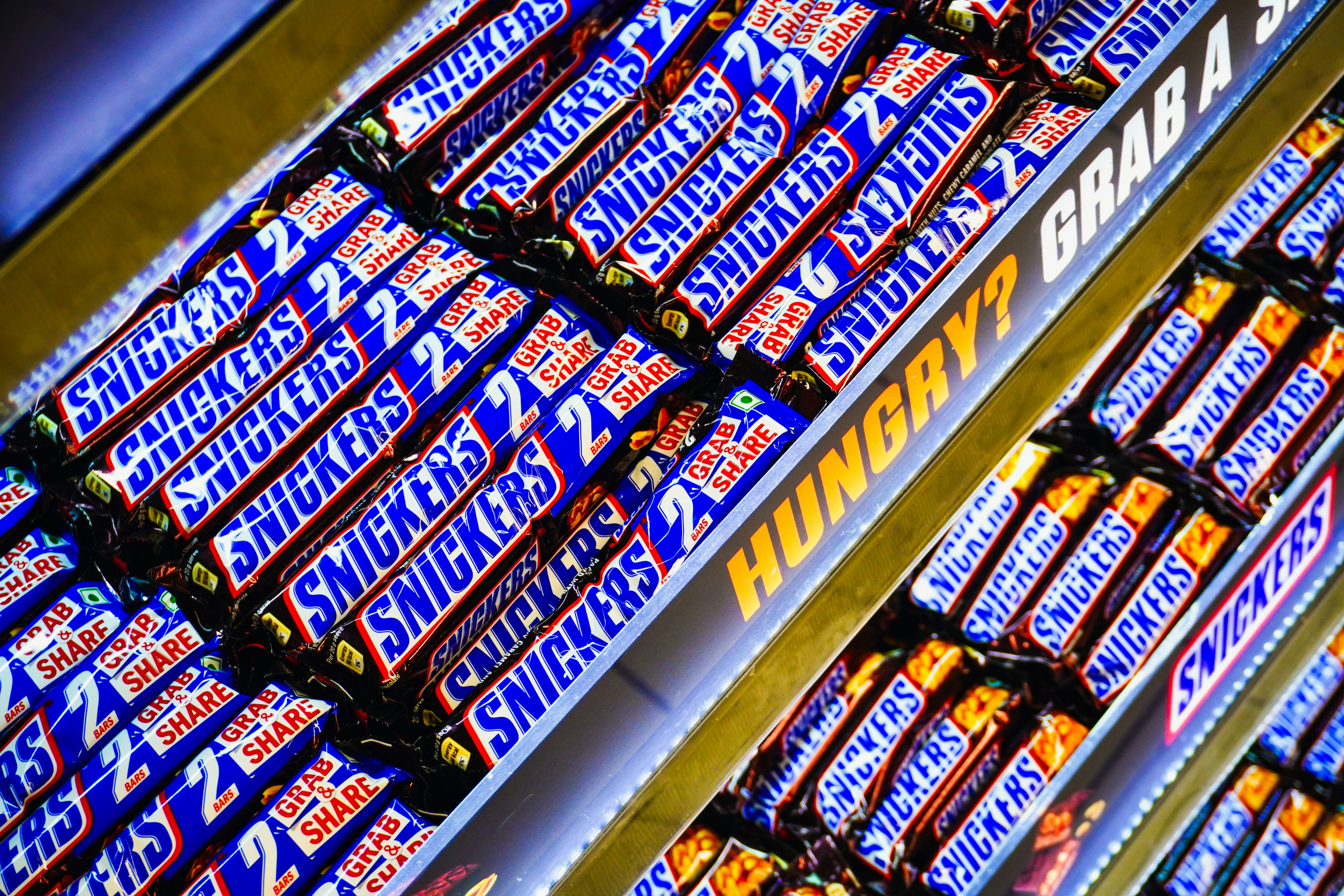 Close-up view of stacked Snickers bars in a store display, with bold blue packaging creating a dense, repeating pattern.