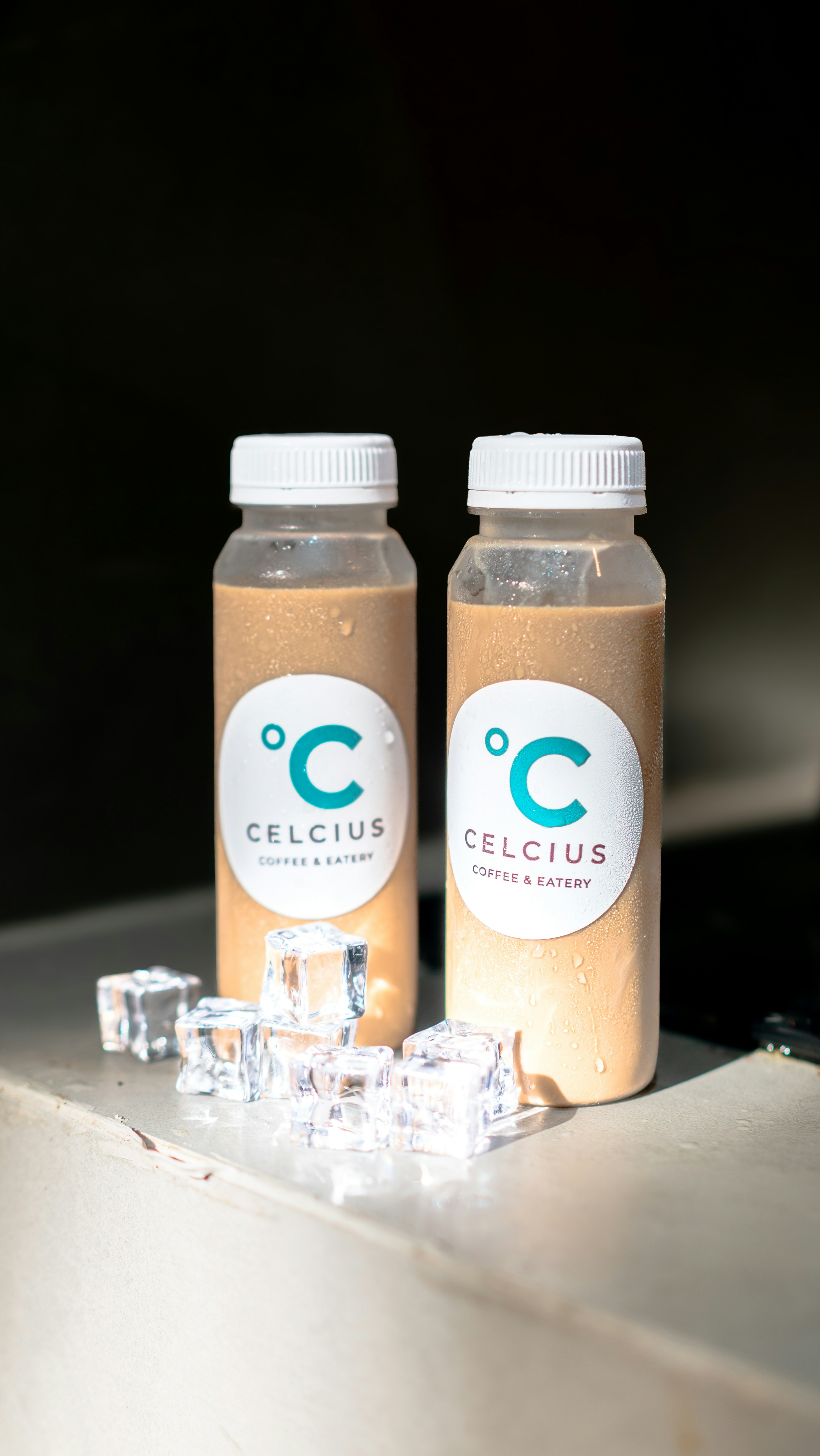 Two Bottles of Celcius Iced Coffee Stand Proudly with Ice Cubes in Foreground